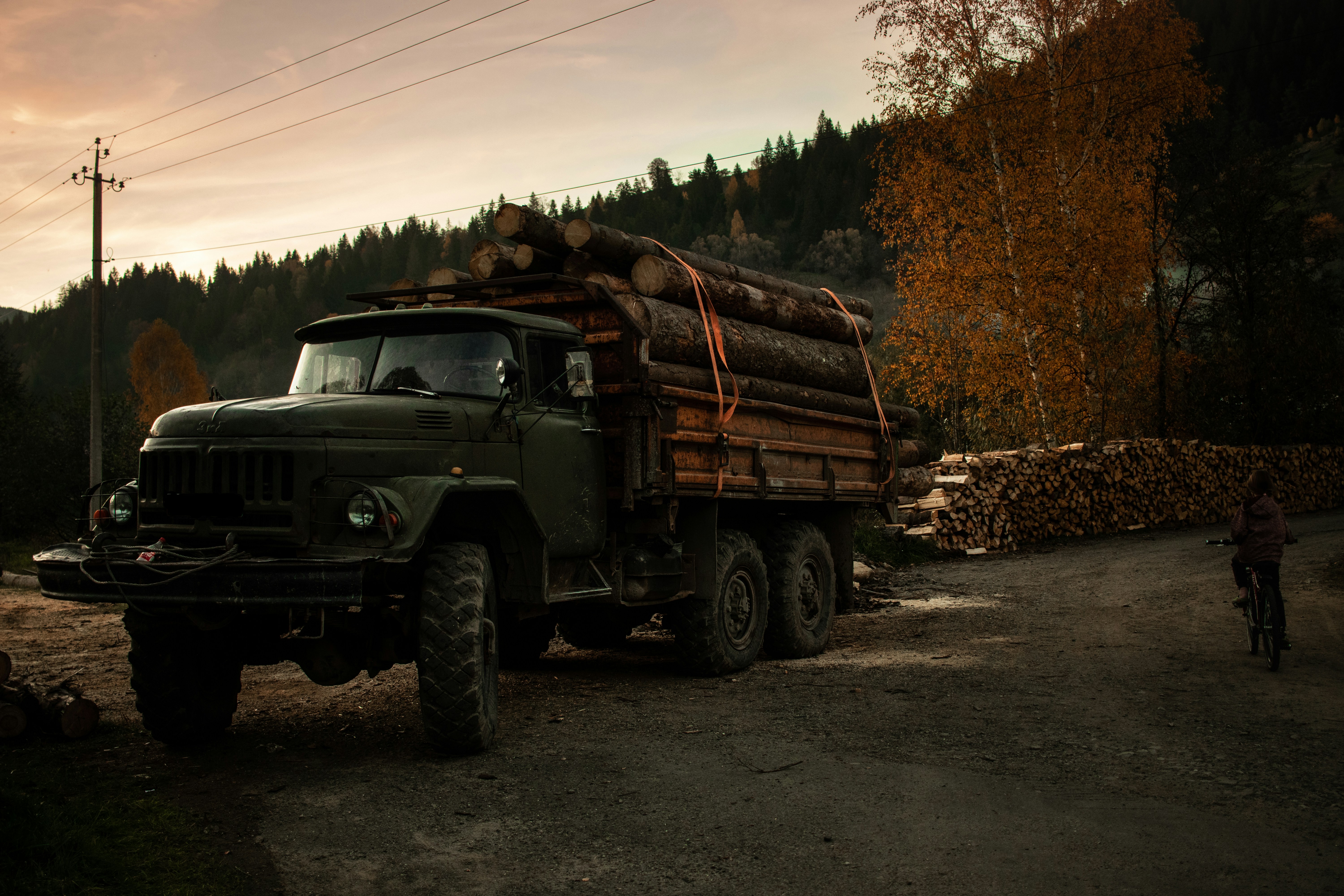 Heavy-duty truck loaded with logs parked on a gravel road, surrounded by autumn foliage and twilight hues.