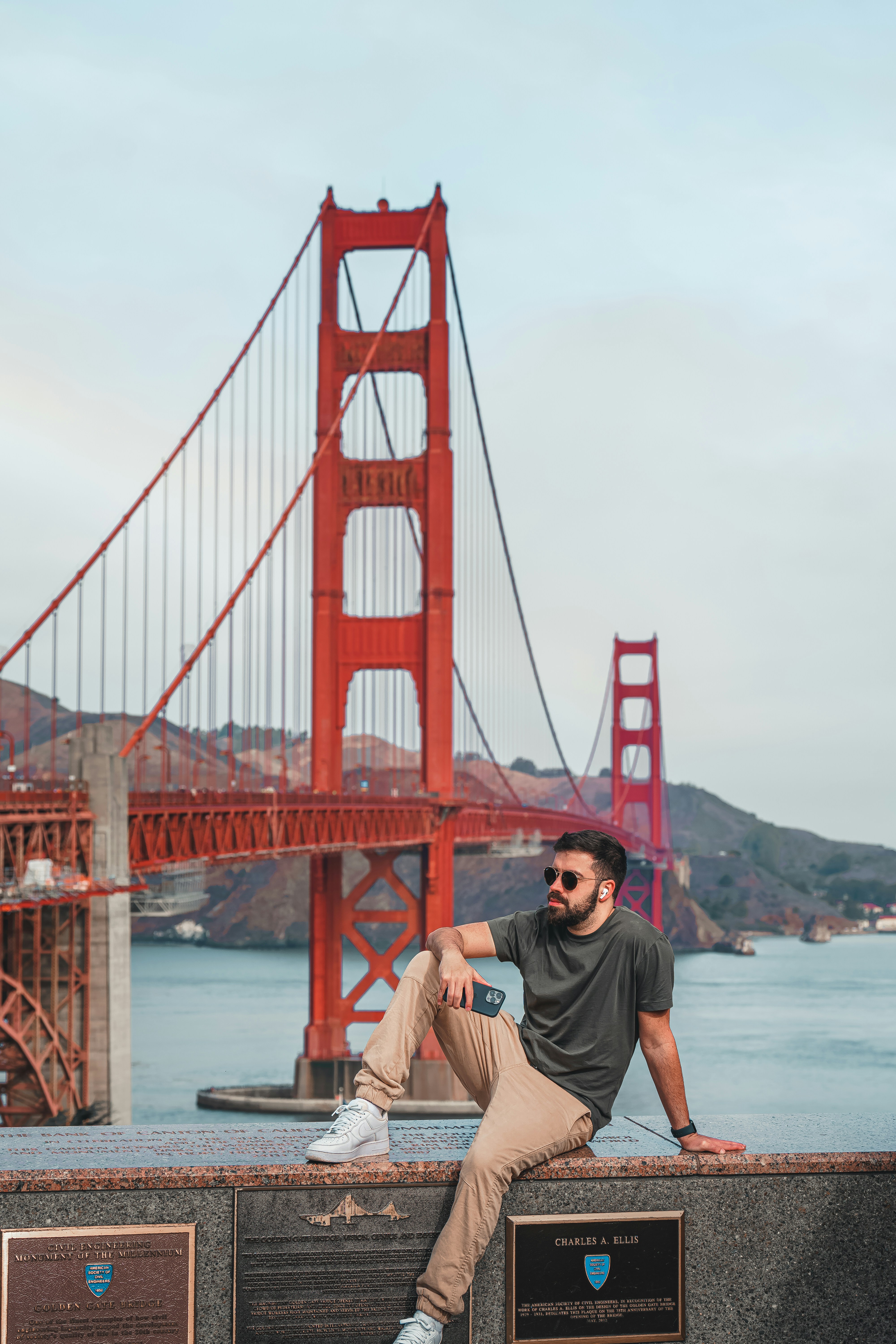 A man sitting on a ledge in front of a large red bridge with Golden ...