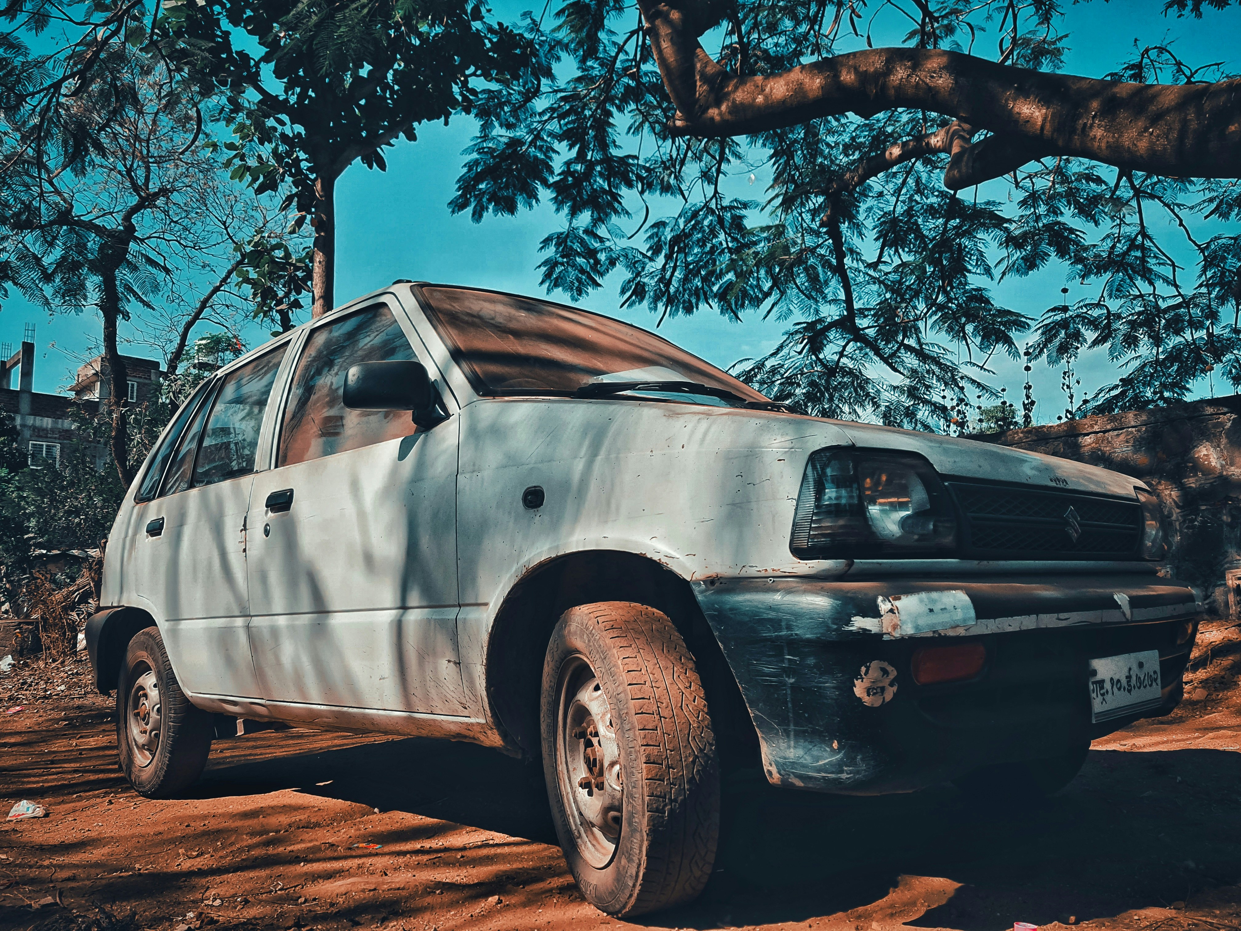 Vintage car parked under a tree, showcasing its weathered exterior against a backdrop of vibrant foliage.