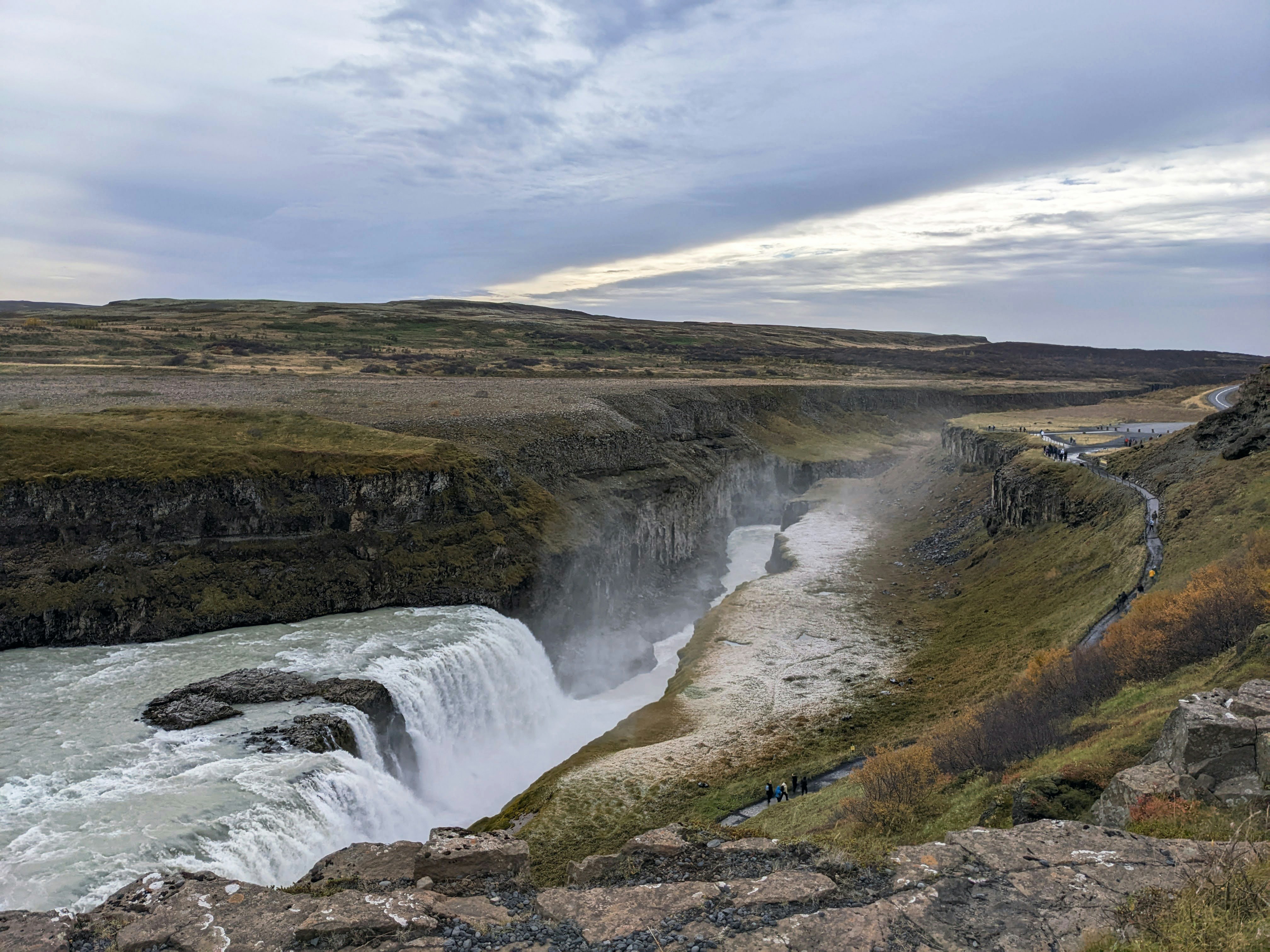 Majestic waterfall plunging into a rugged canyon, surrounded by lush greenery and a winding path. Mist rises from the falls, creating an ethereal atmosphere.