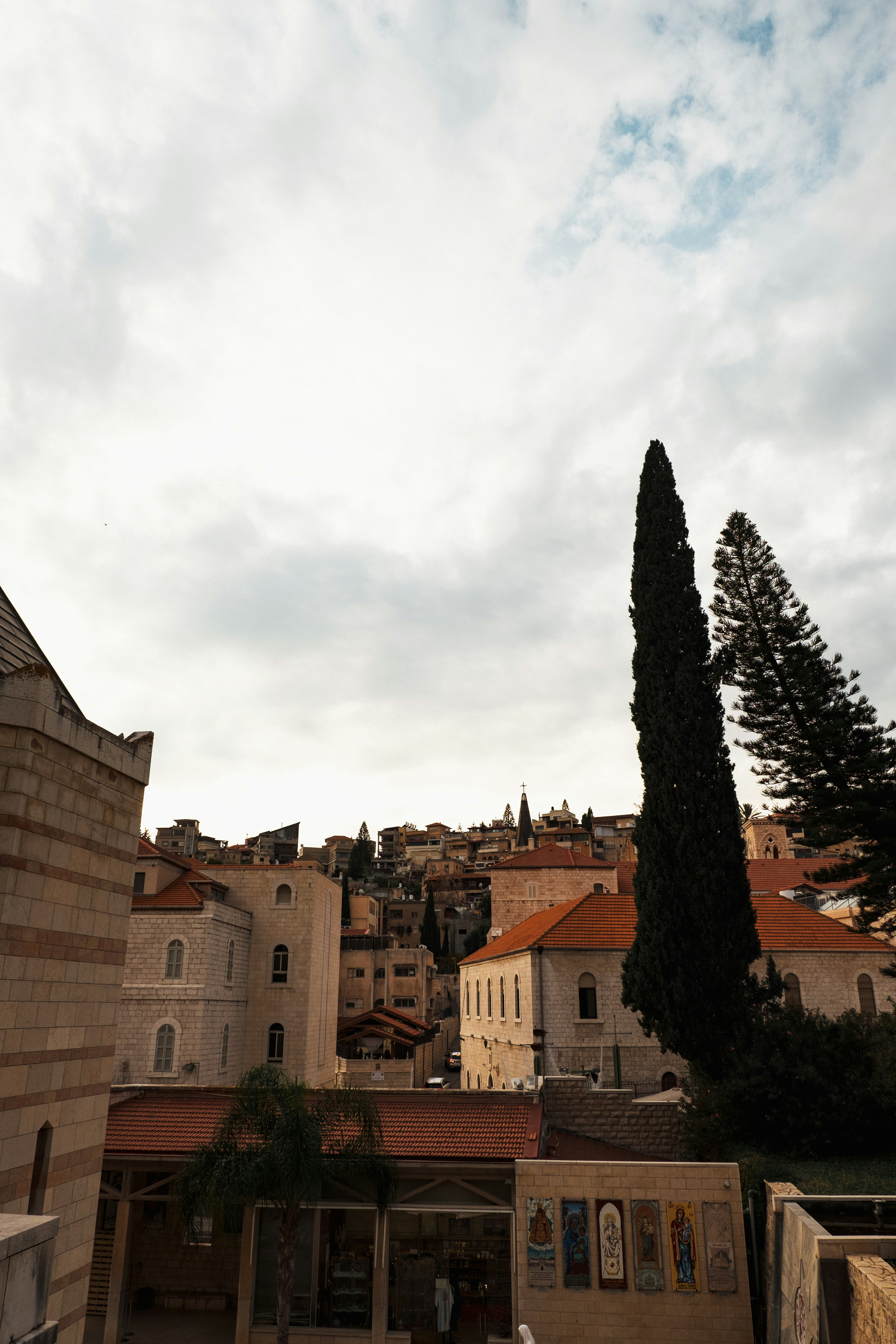 Historic stone buildings rise amidst lush greenery under a cloudy sky, showcasing a blend of architectural styles. The scene evokes a sense of nostalgia and cultural richness.