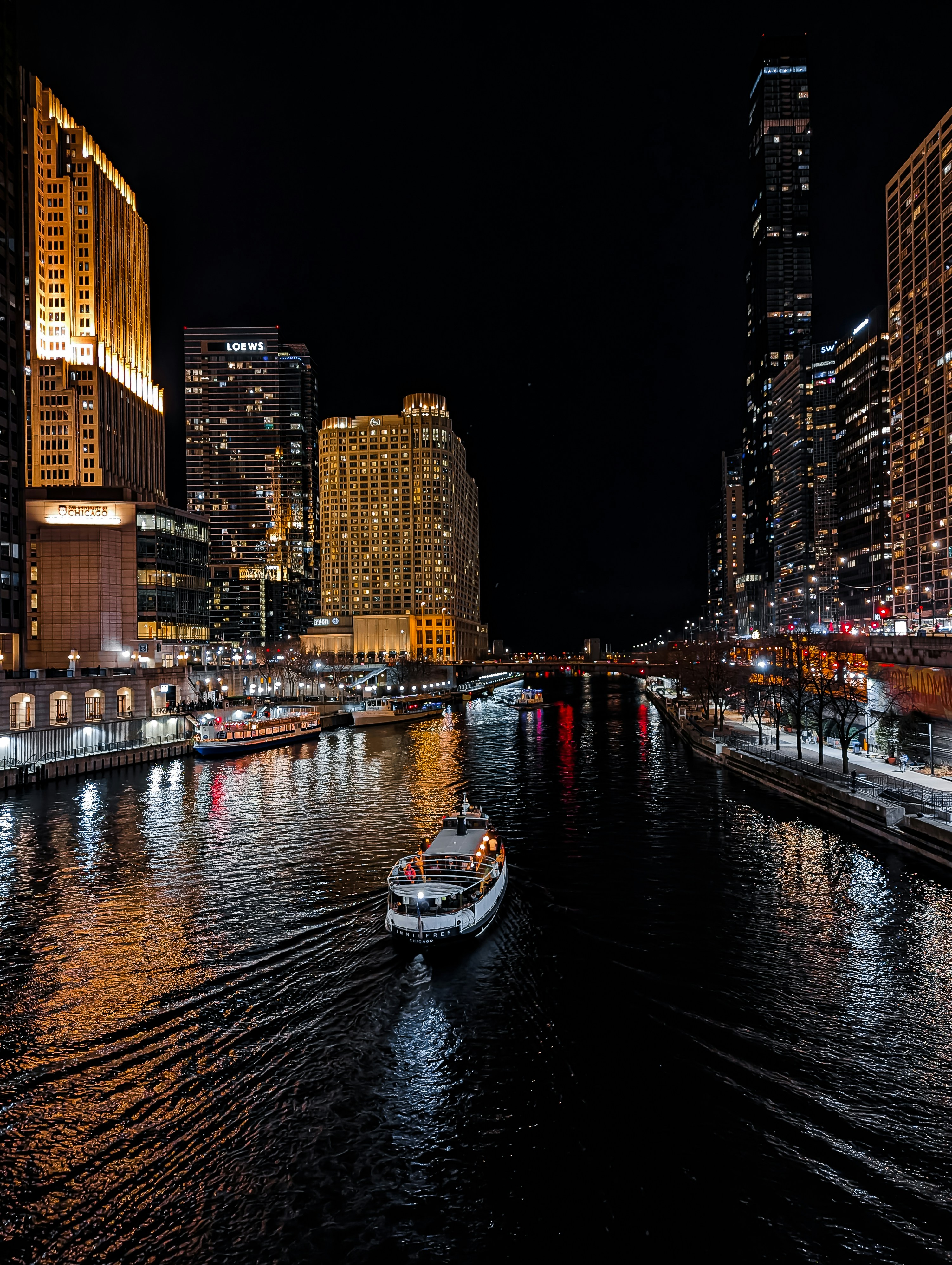 Nighttime city canal with illuminated buildings and a boat cruising the water; a urban waterway scene highlighting reflections and artificial lights.