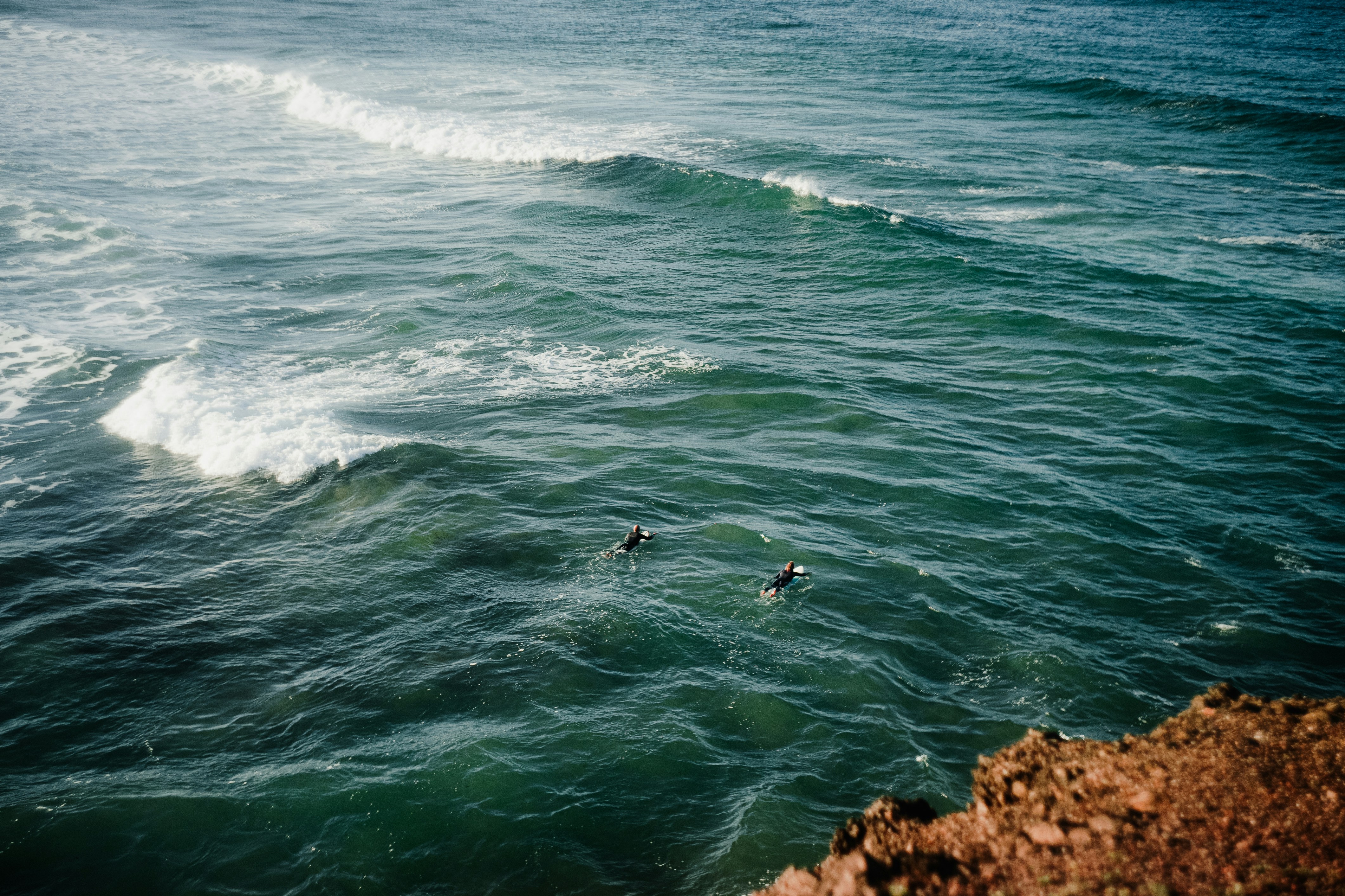 Emerald Swell from the Cliff: Two Surfers in Quiet Transit