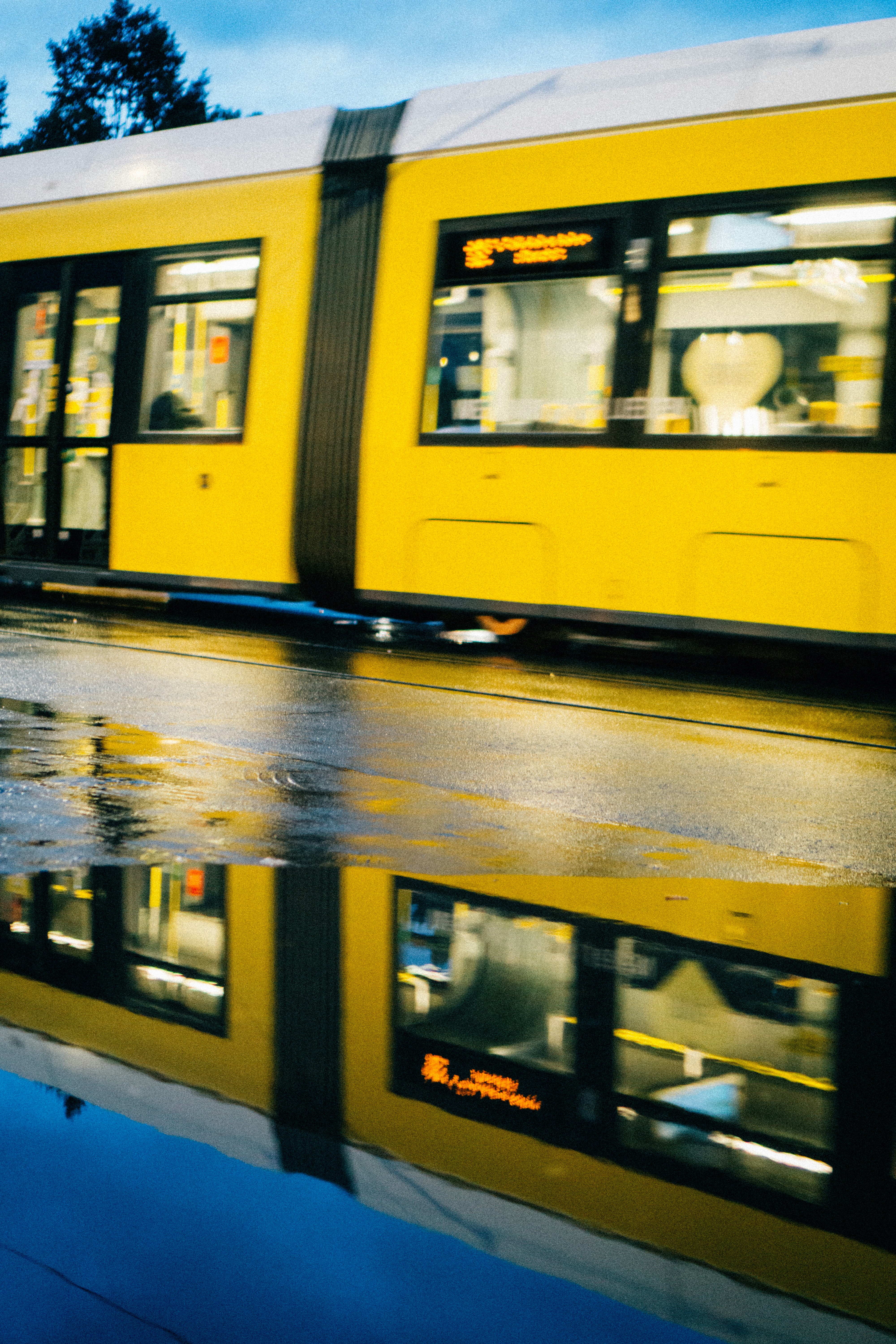 A yellow train traveling down train tracks next to a puddle photo ...
