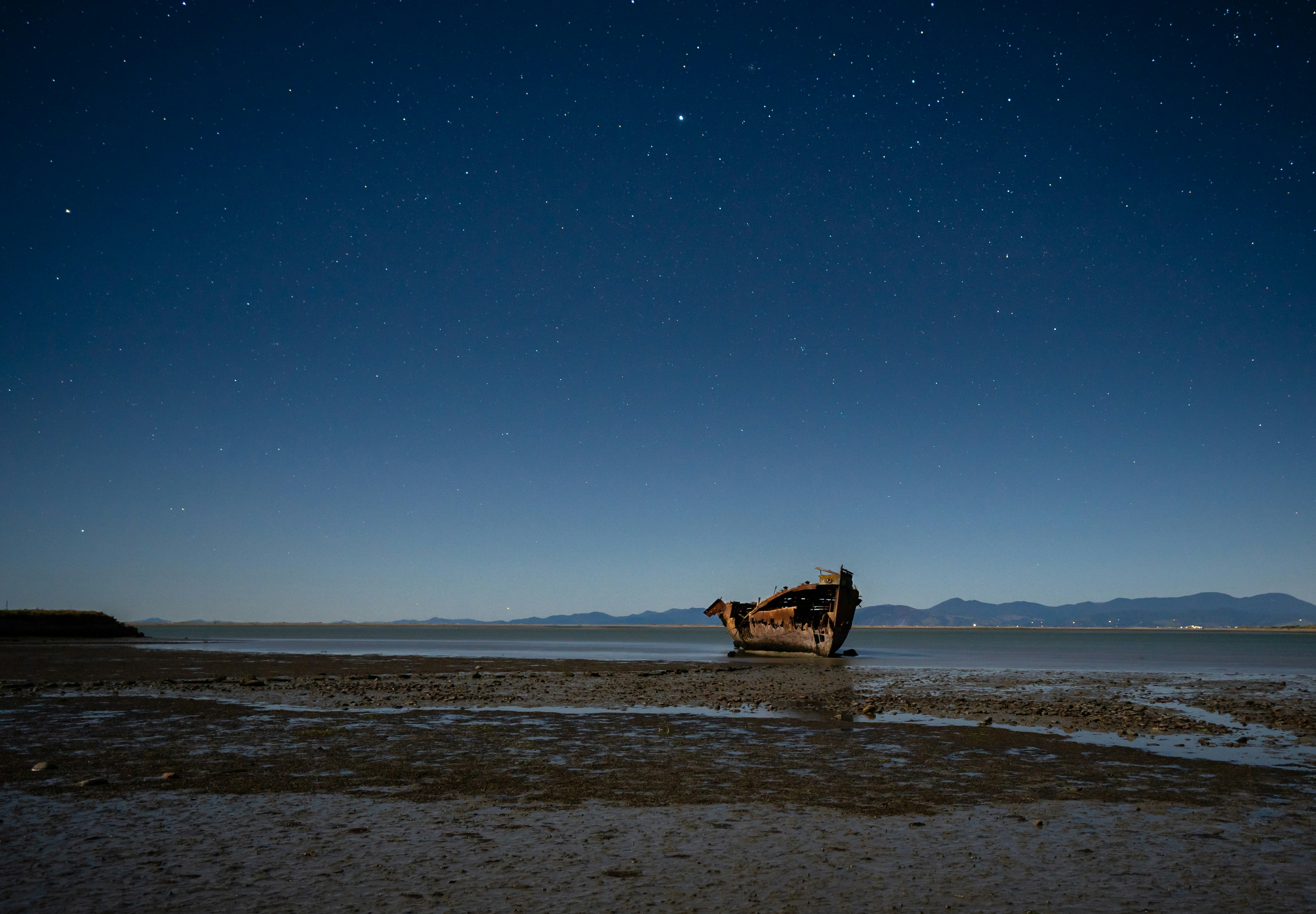 An abandoned ship rests on the muddy shore beneath a vast starry sky, evoking a sense of nostalgia and tranquility.
