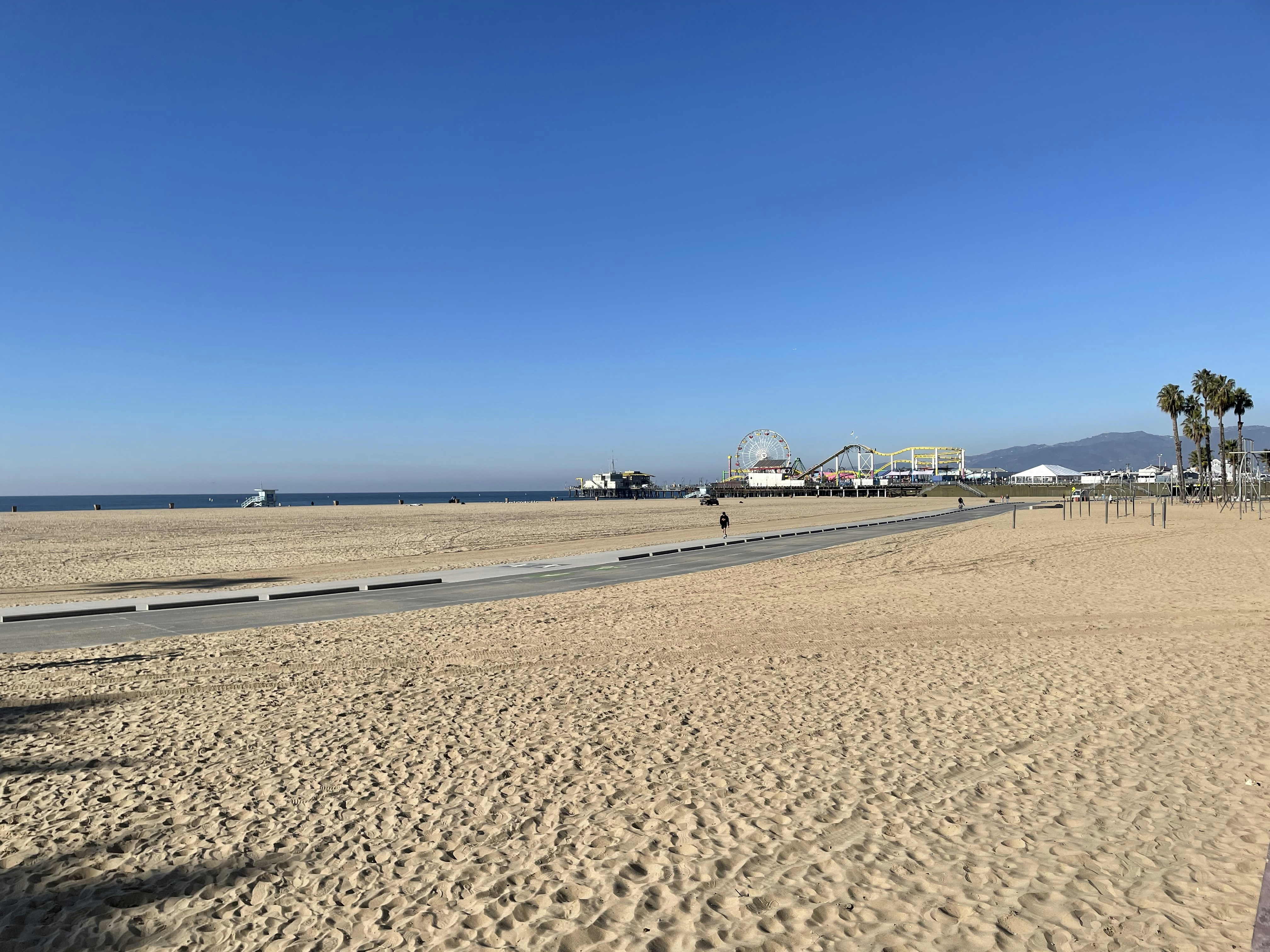 A sandy beach with a roller coaster in the distance photo – Free ...