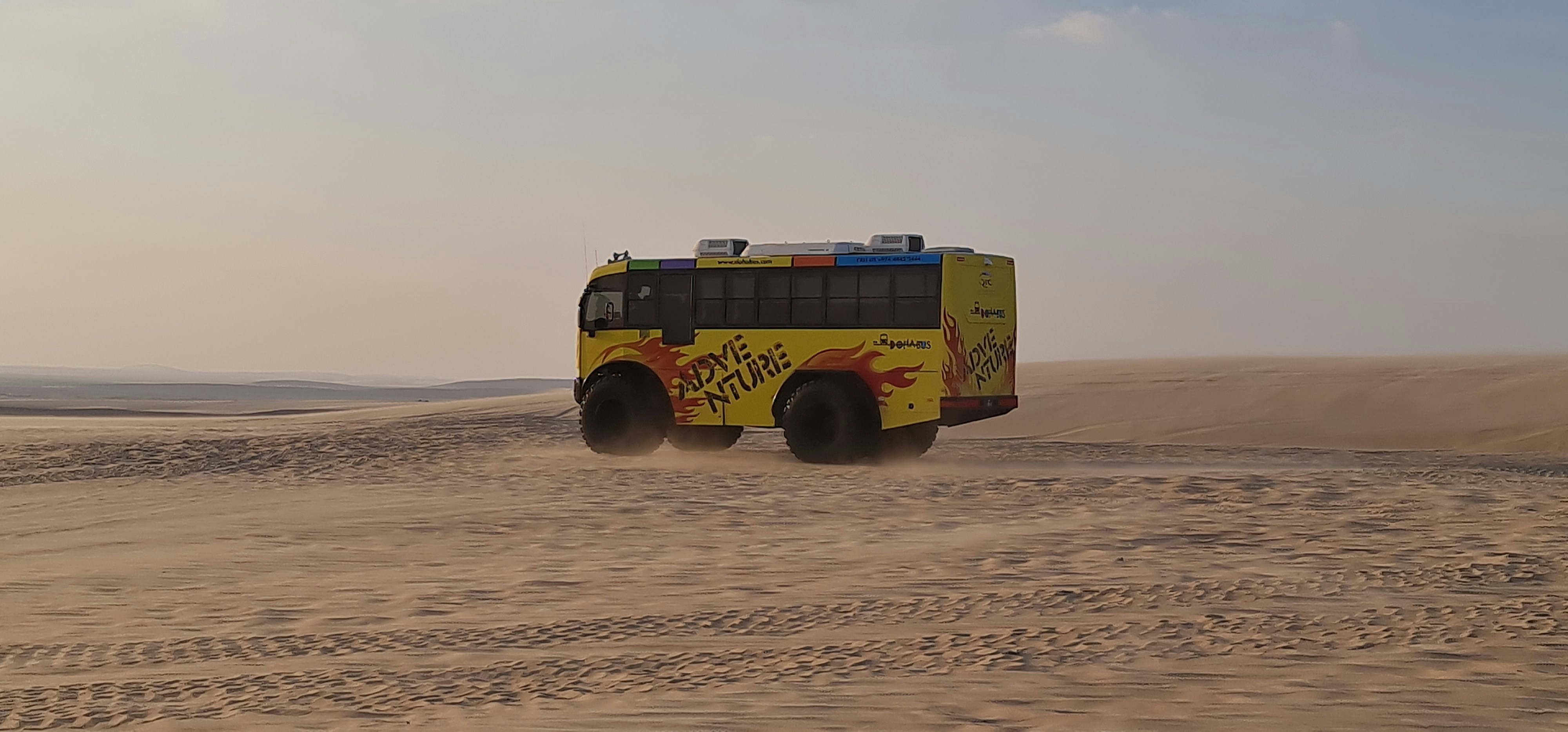 A yellow bus driving through a sandy desert photo – Free Qatar Image on ...