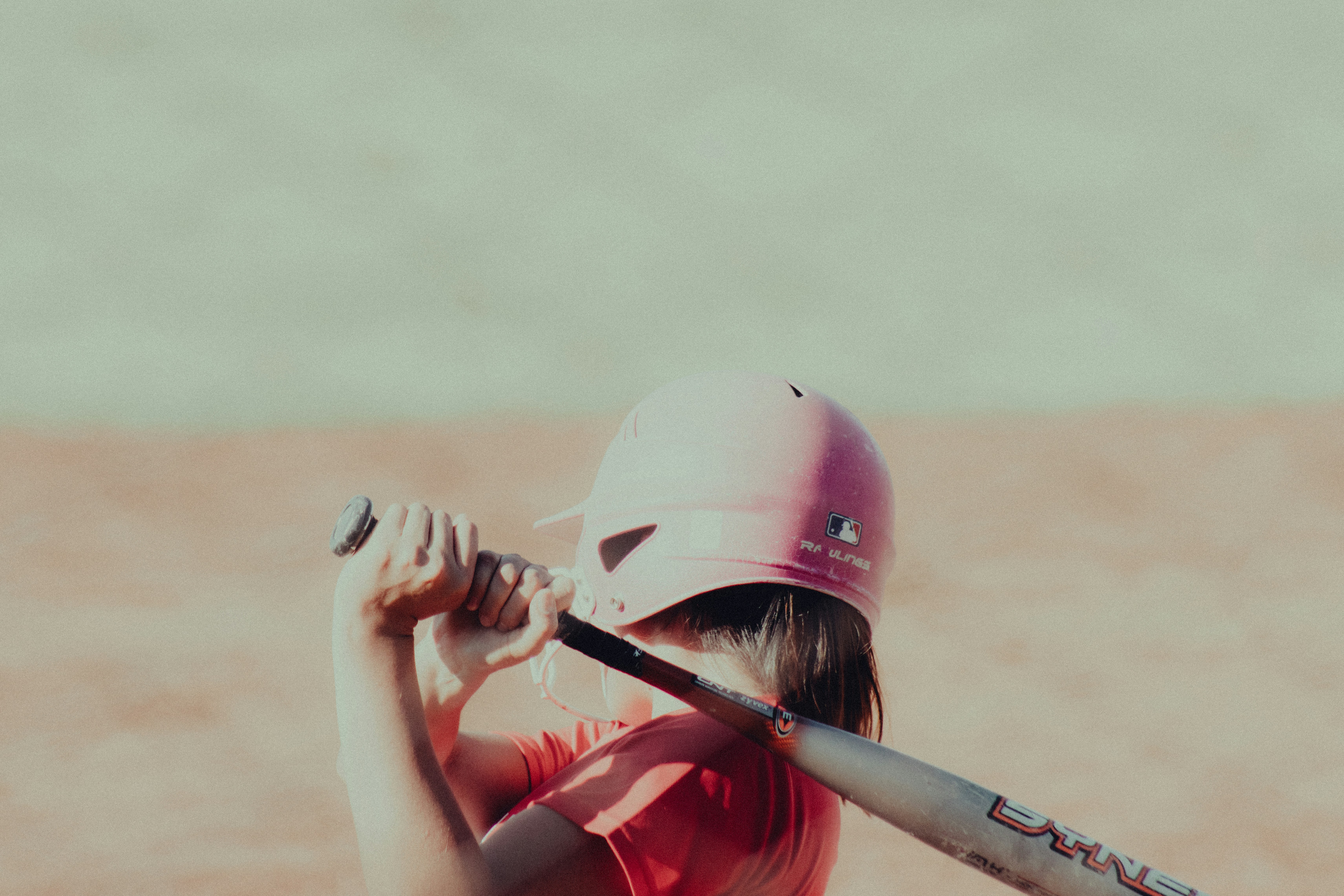 Pink helmet, red jersey: a batter mid-swing against a dusty backdrop