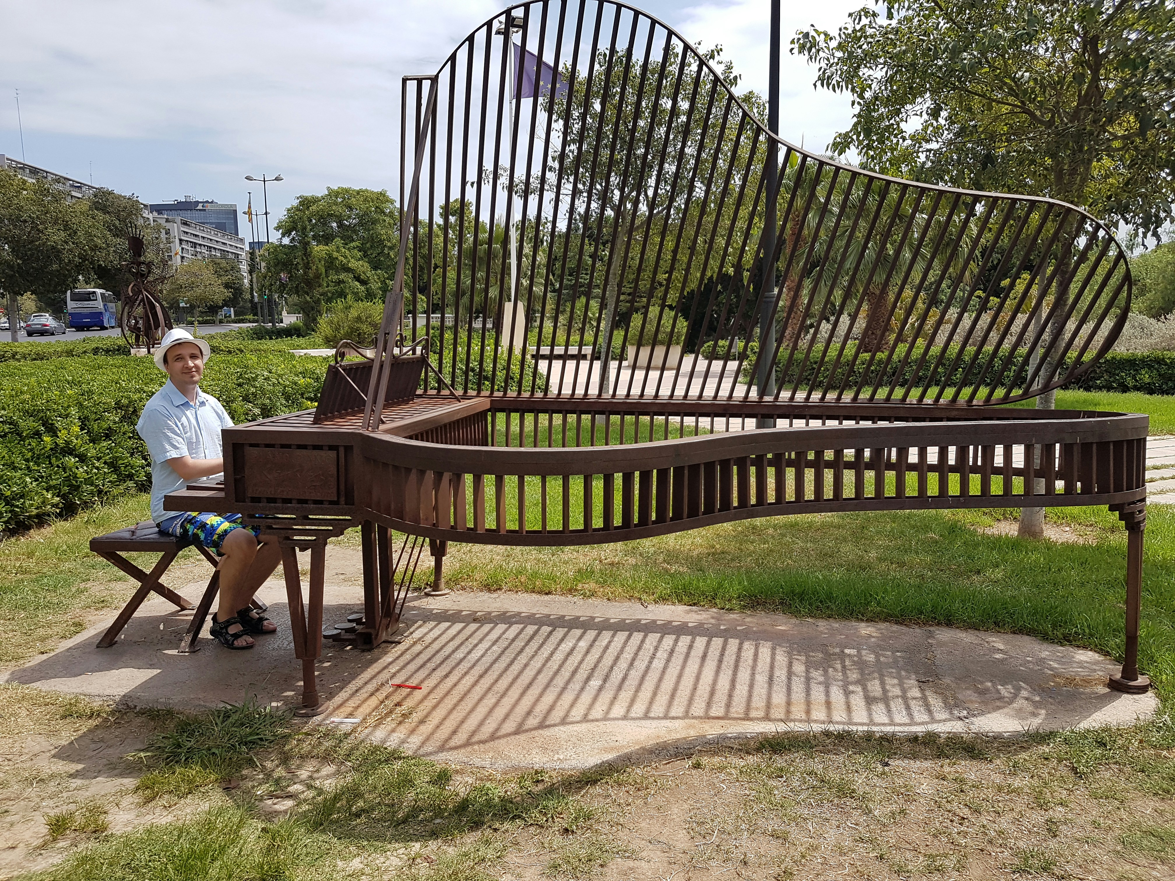 Parkside Pianist: A Man at a Giant Metal Grand Piano Under Sunlit Skies