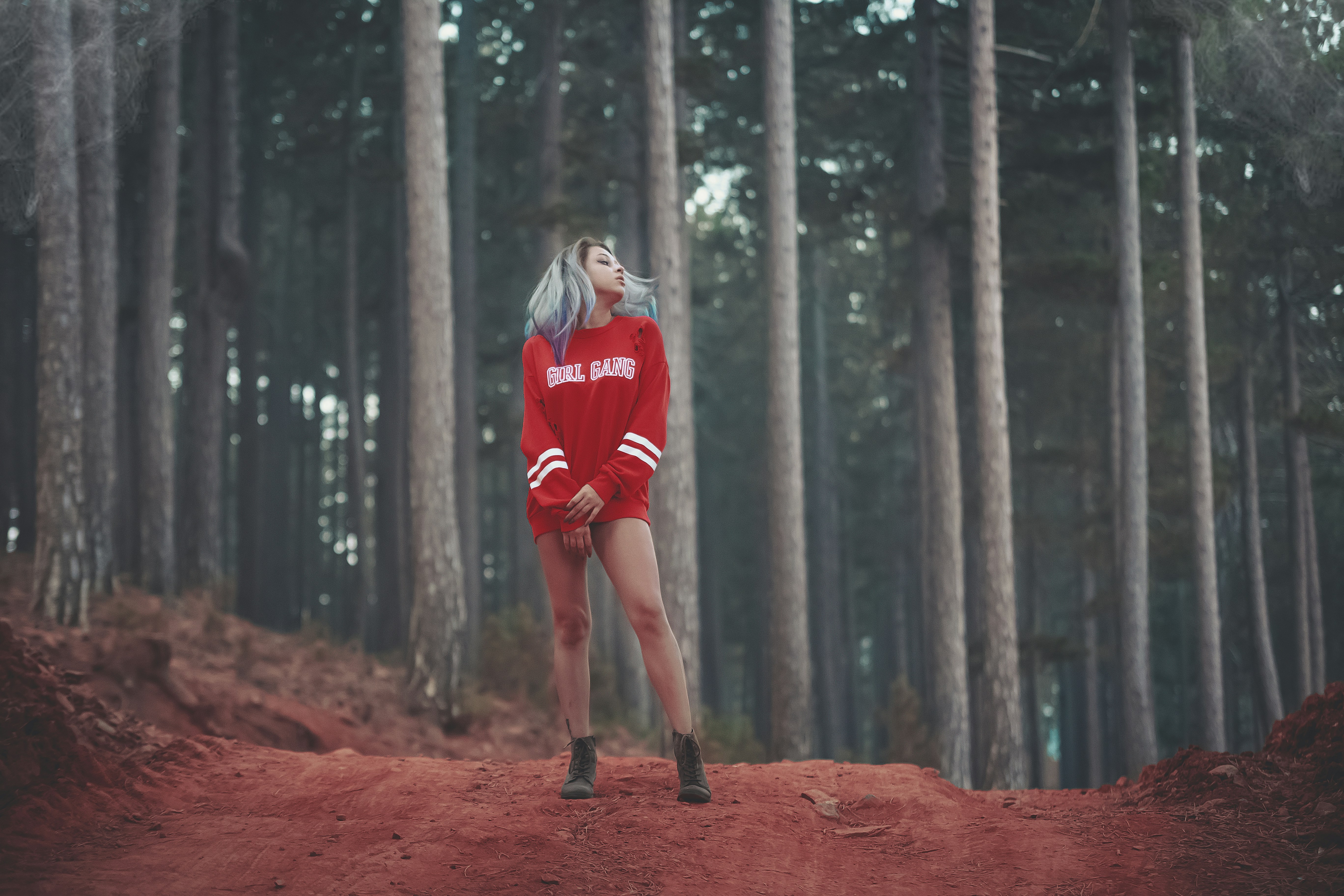 Portrait of a blue-haired girl in a red mini dress standing in the middle of the forest. Red earths, dark green forest and a clear composition that emerges.