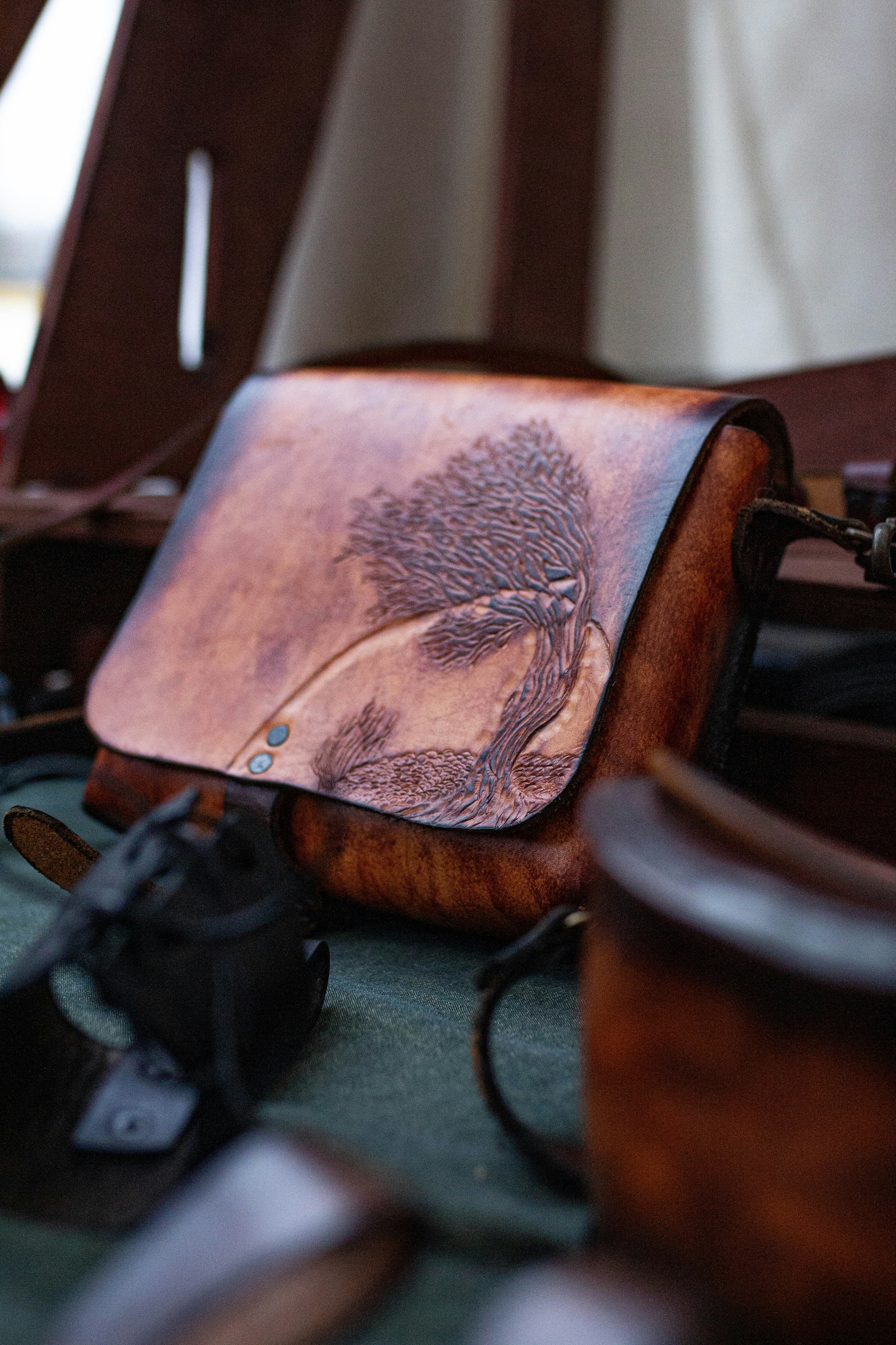 Close-up photograph of a brown leather bag with an embossed pine tree motif resting on a desk.