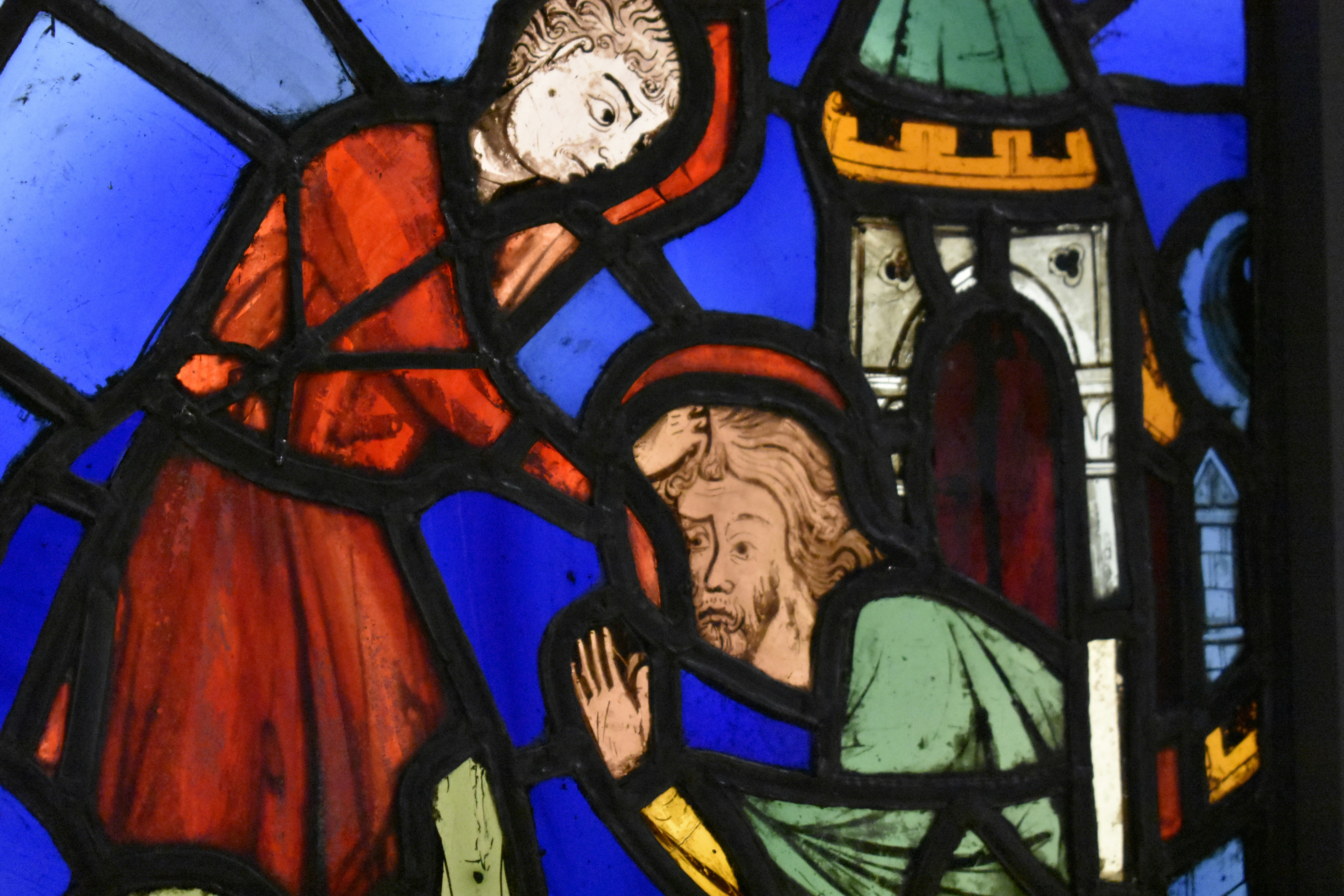 Medieval stained glass scene depicting two figures in vibrant robes, set against a deep blue background.