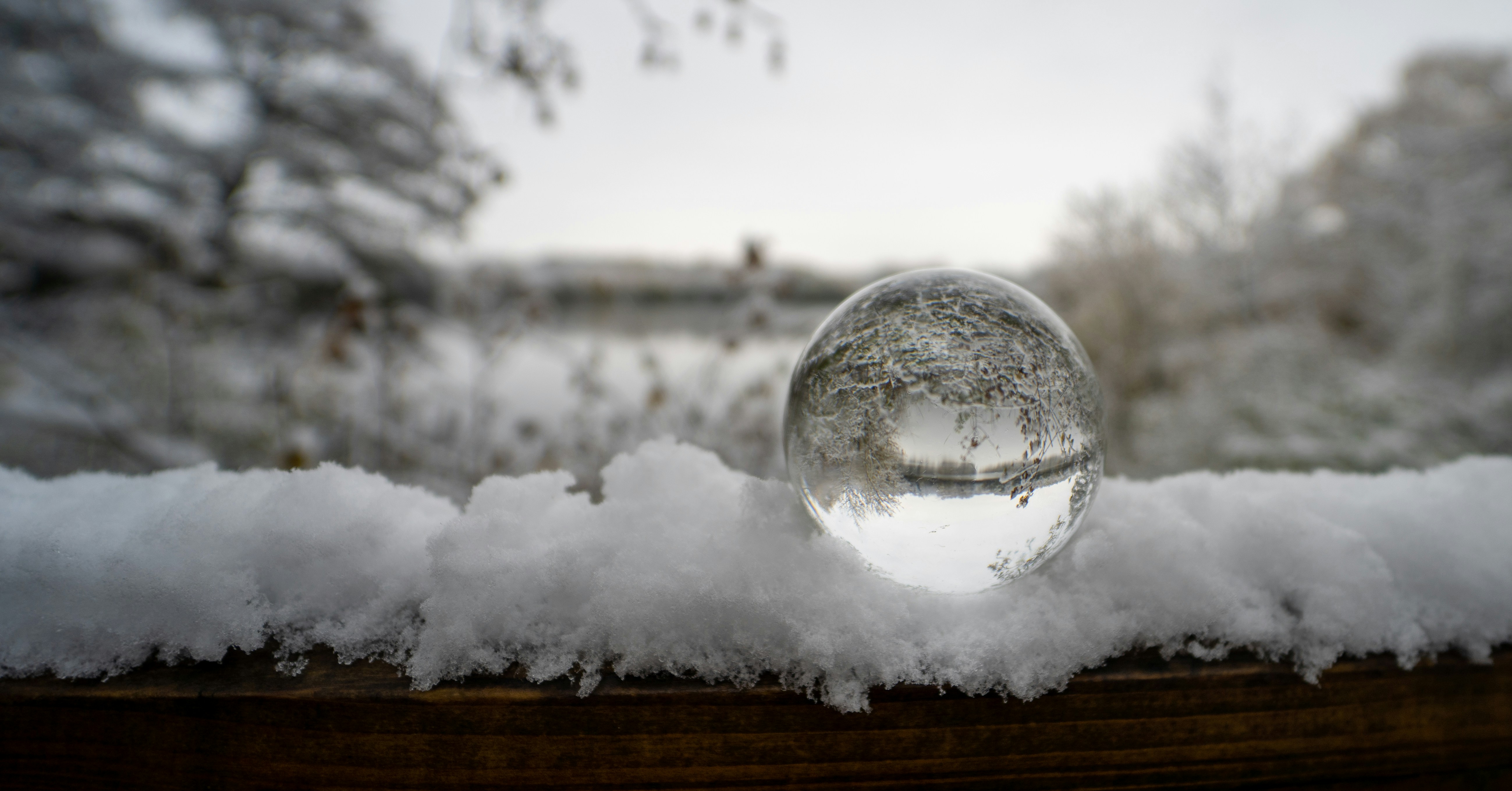 Glass orb resting on snow-covered surface with blurred winter landscape in the background.