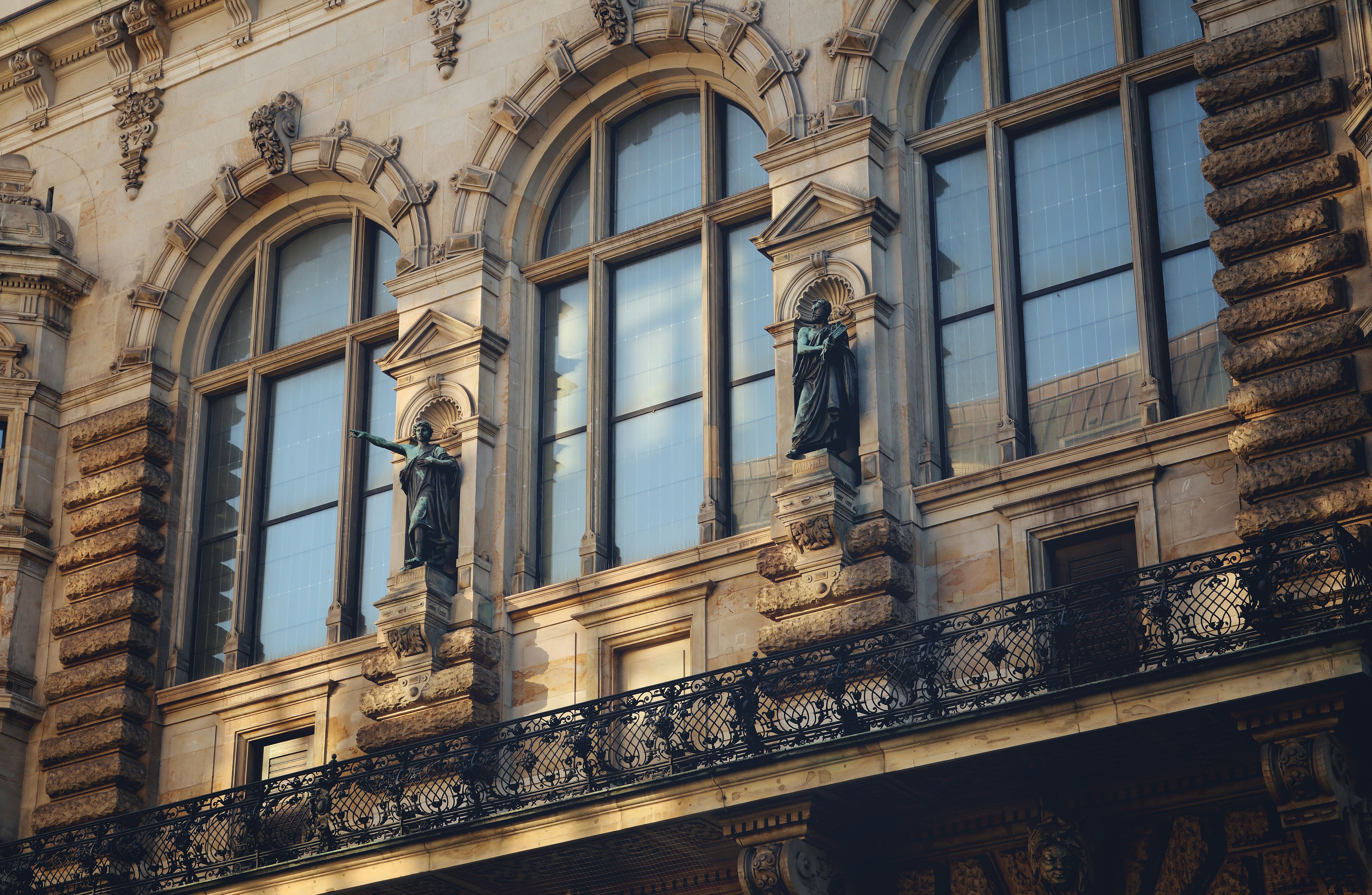 Statues flanking ornate windows of a historic building, showcasing intricate architectural details and artistry.