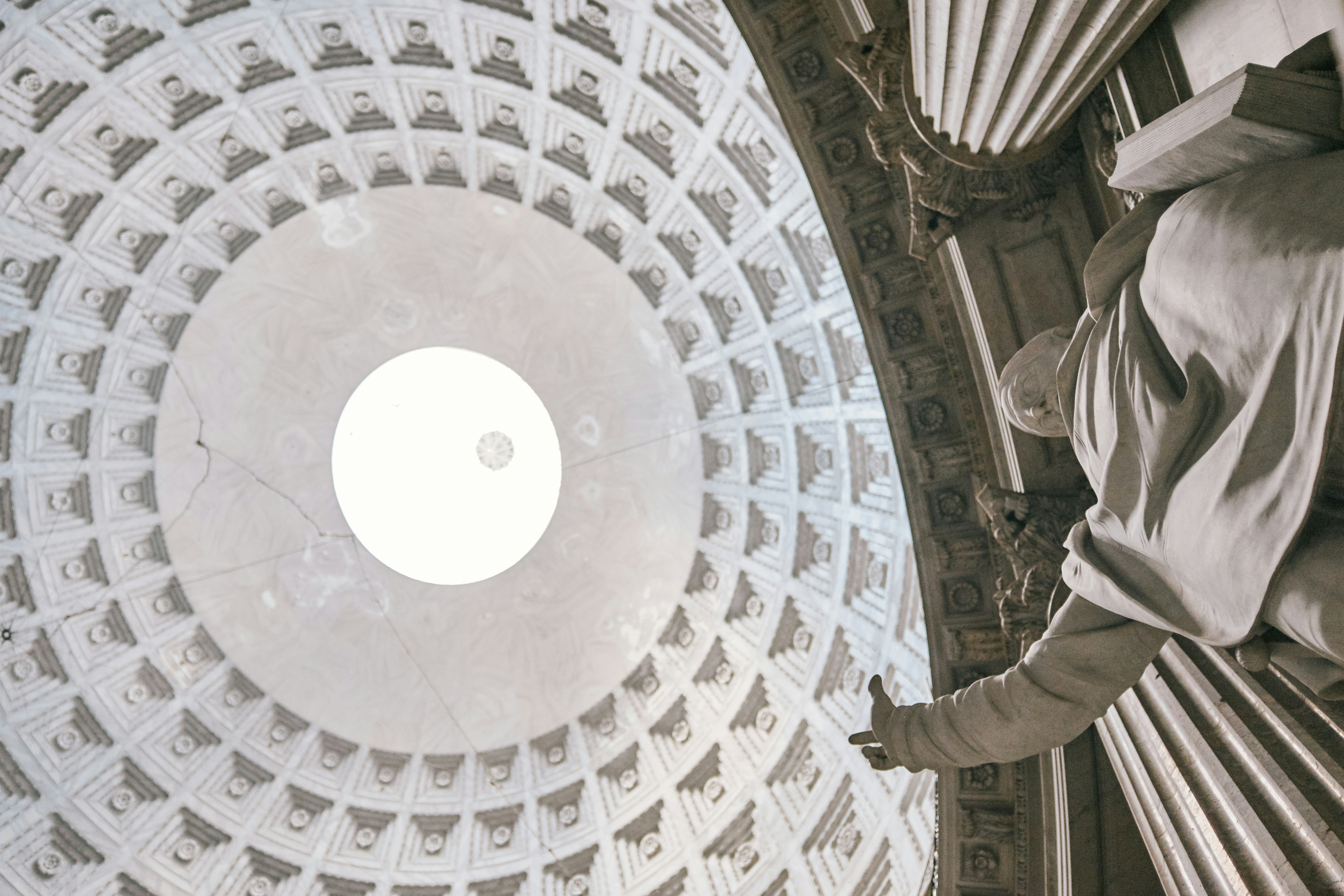 Statue inside the Pantheon gazing upward towards the patterned dome and central oculus.