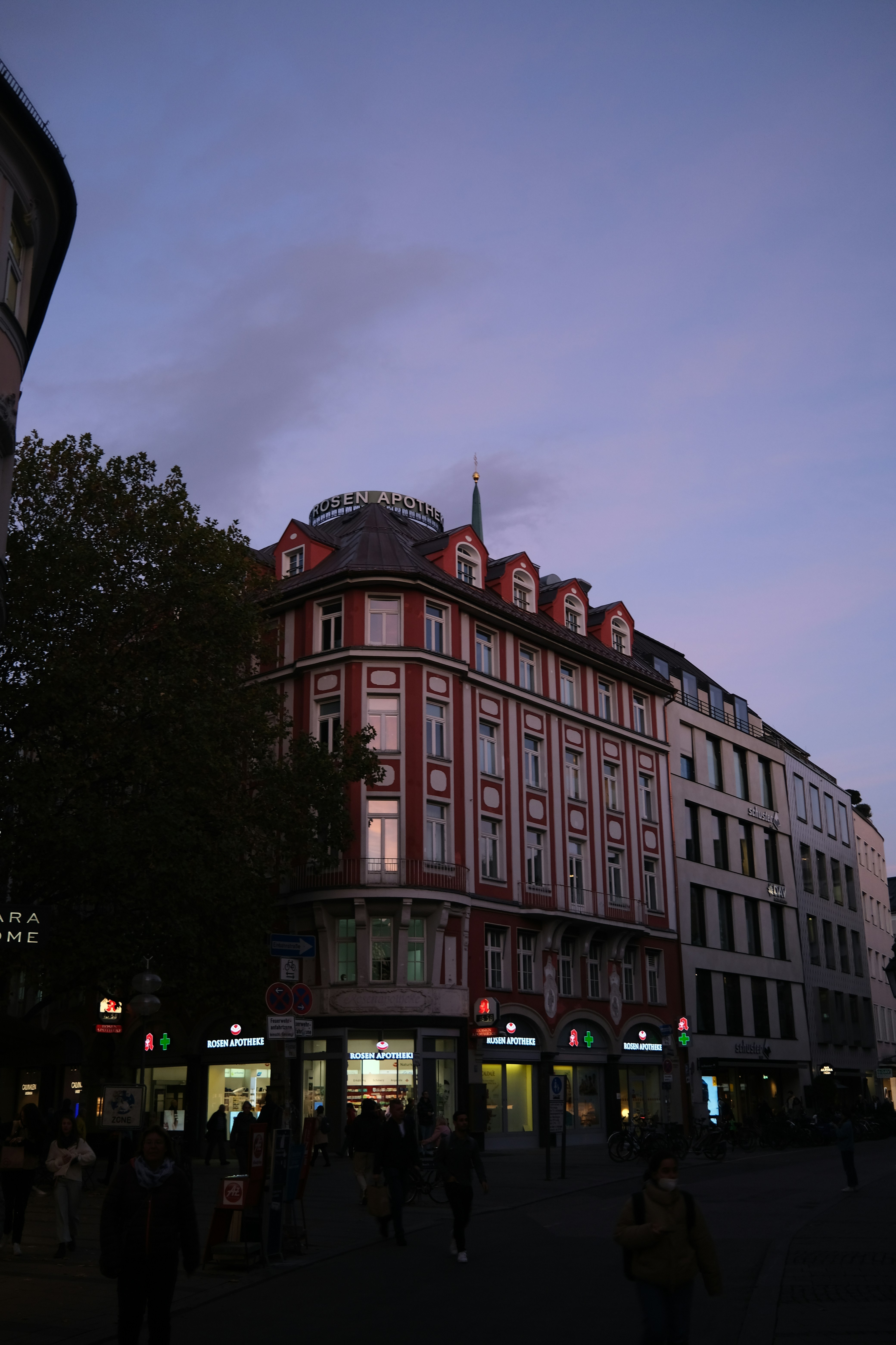 Historic building with ornate red and white architecture illuminated at twilight, surrounded by urban life.