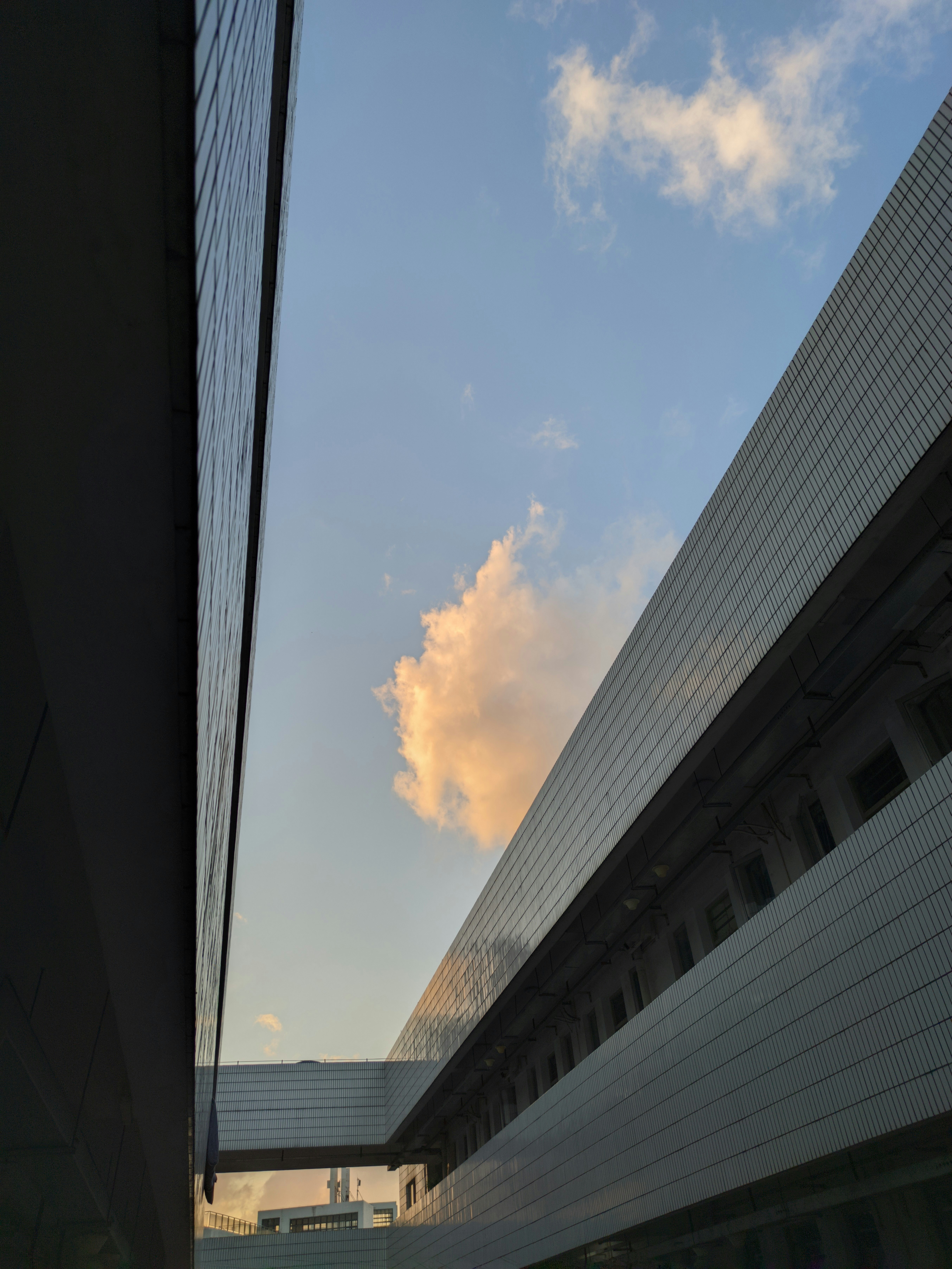 Reflections of modern architecture frame a soft, wispy cloud against a serene sky.