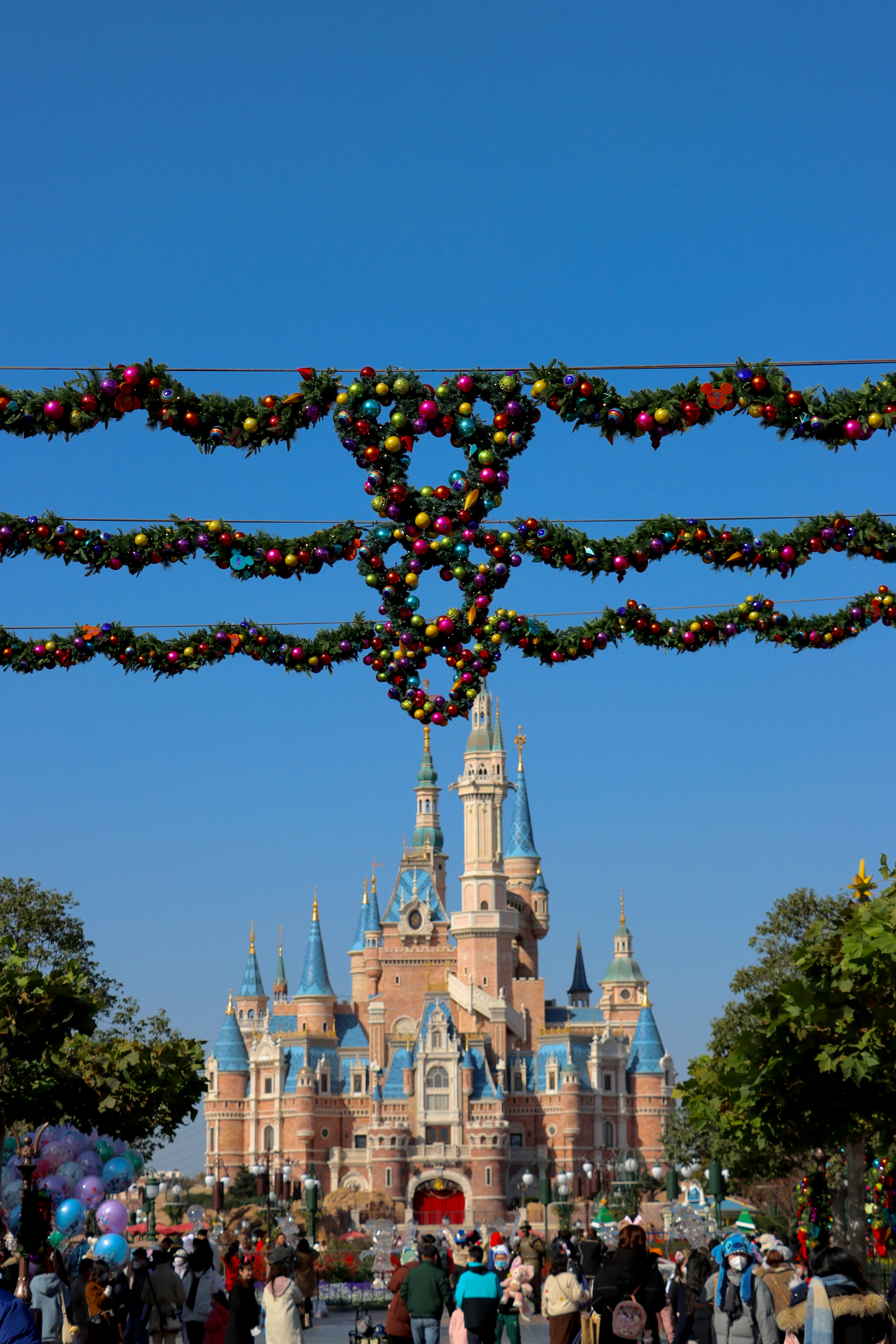 Festively adorned castle surrounded by cheerful visitors in a vibrant theme park setting. Colorful decorations enhance the magical atmosphere.