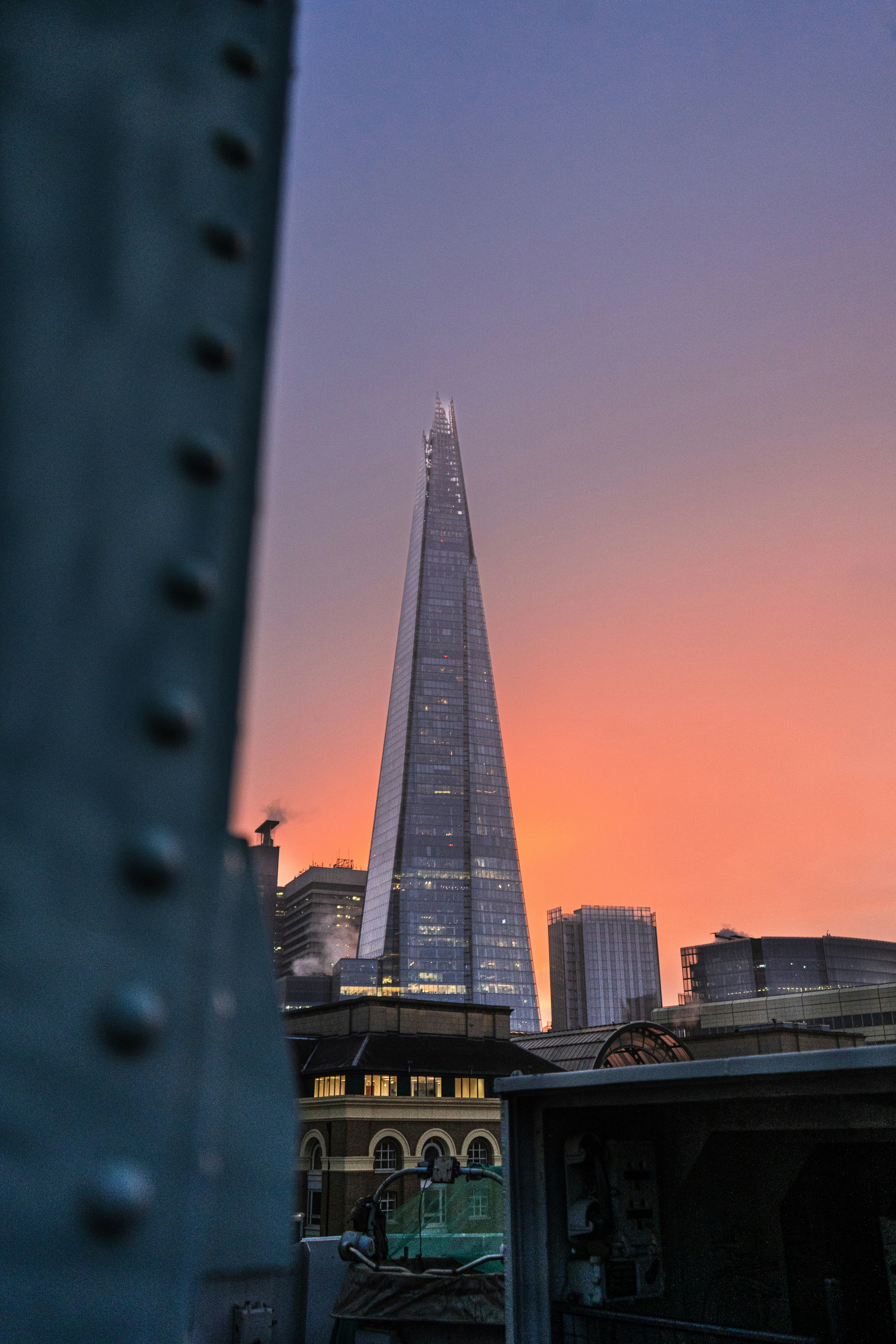 The Shard pierces the twilight sky, framed by industrial elements, showcasing the contrast between modern architecture and historical structures.