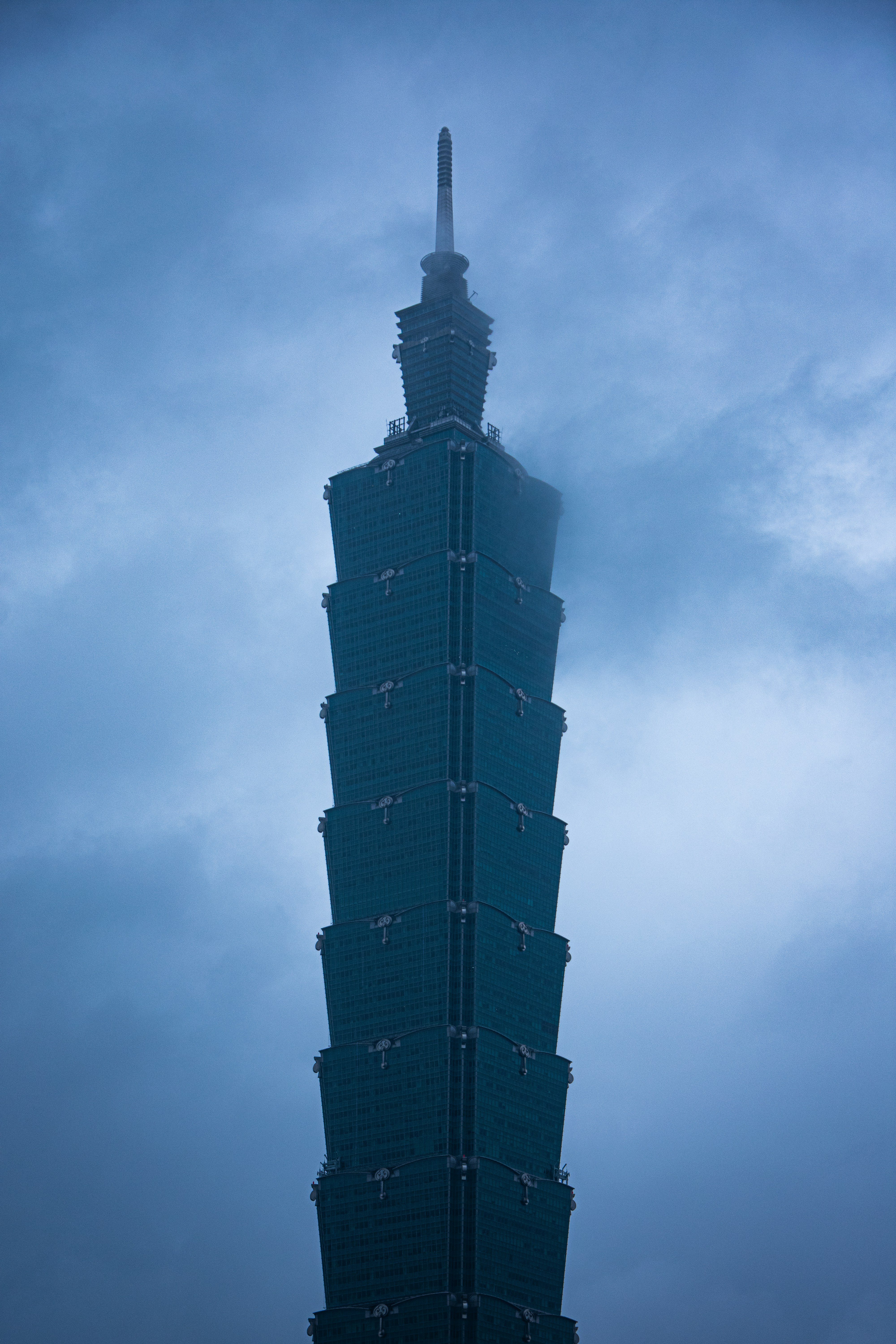 Taipei 101 emerges through a shroud of mist, its distinctive silhouette piercing the cloudy sky. The architectural marvel stands as a testament to modern engineering.