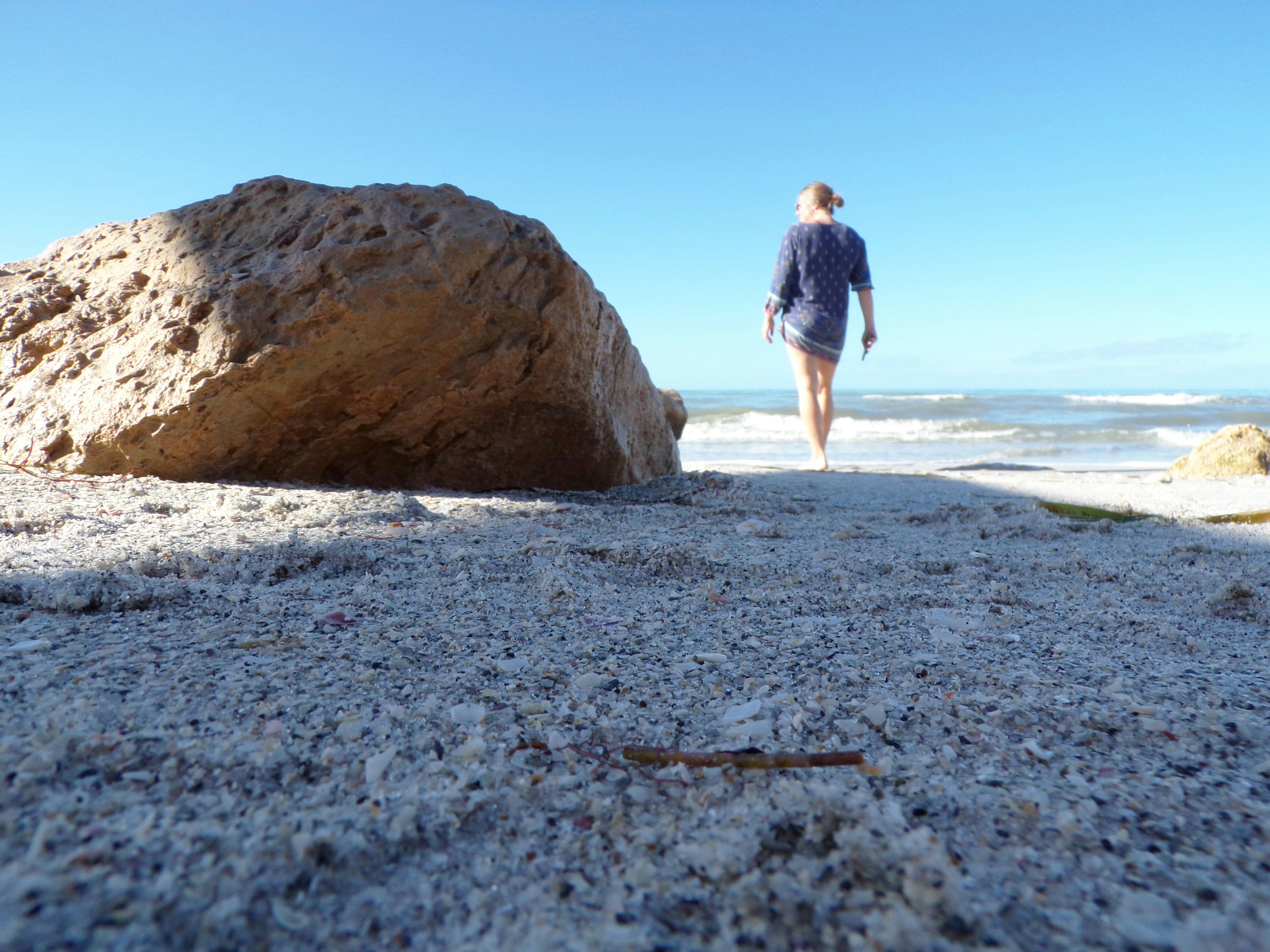A person walking on a beach next to a large rock photo – Free Sunset ...
