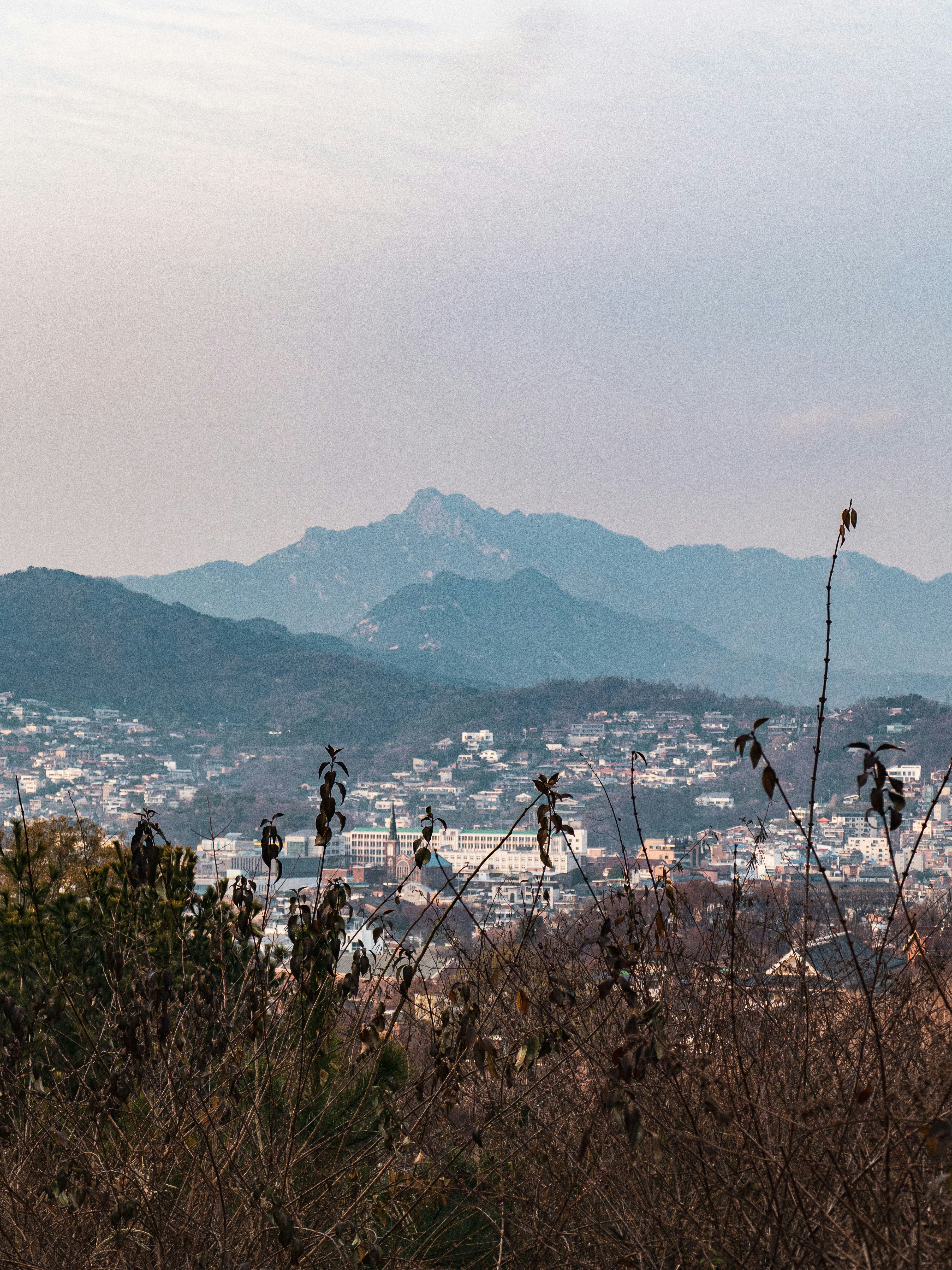A panoramic view of a mountainous landscape at dusk, featuring a blend of urban structures and natural elements. The scene captures the serene transition from day to night.