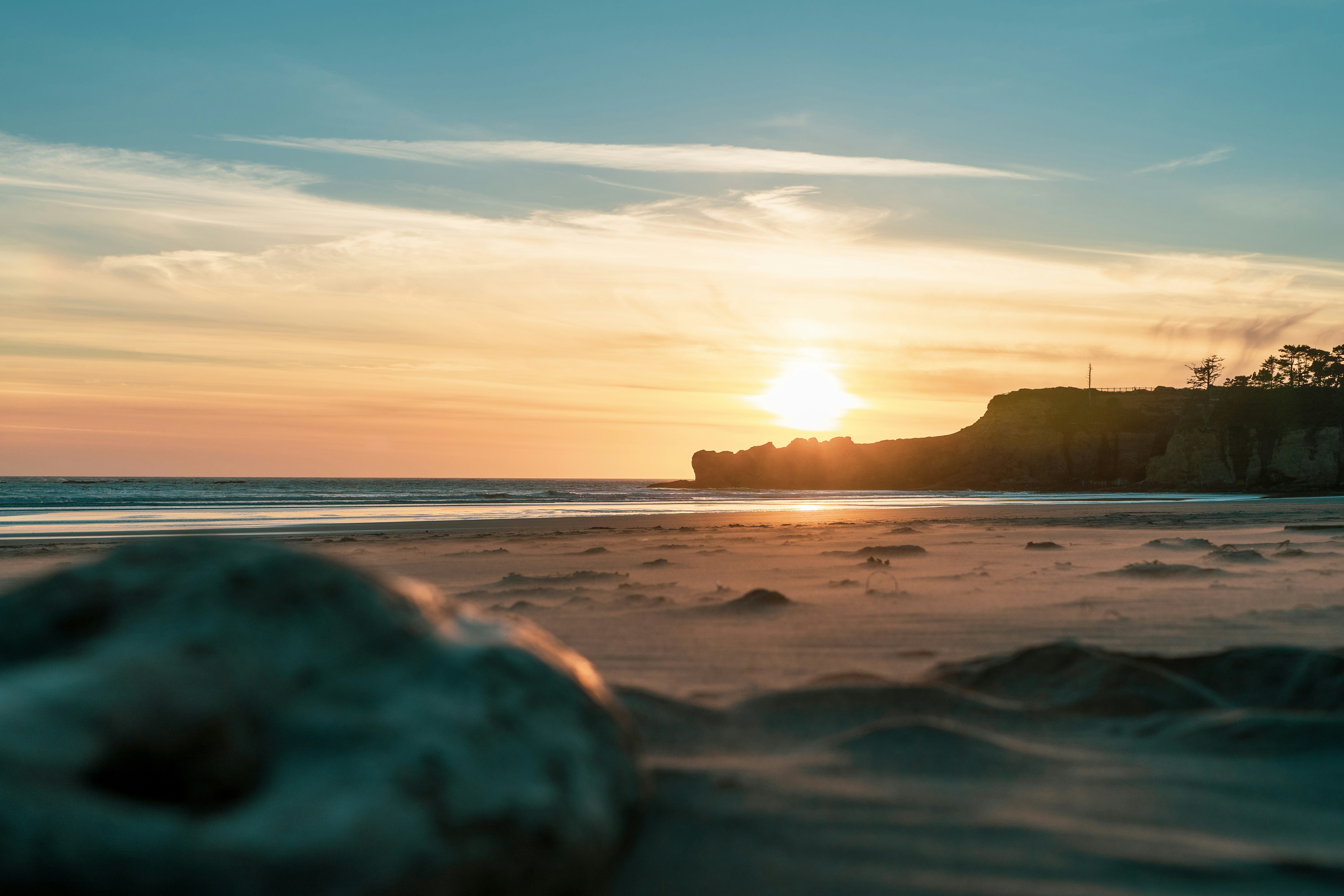 Foto El sol se está poniendo en la playa con una roca en primer plano ...