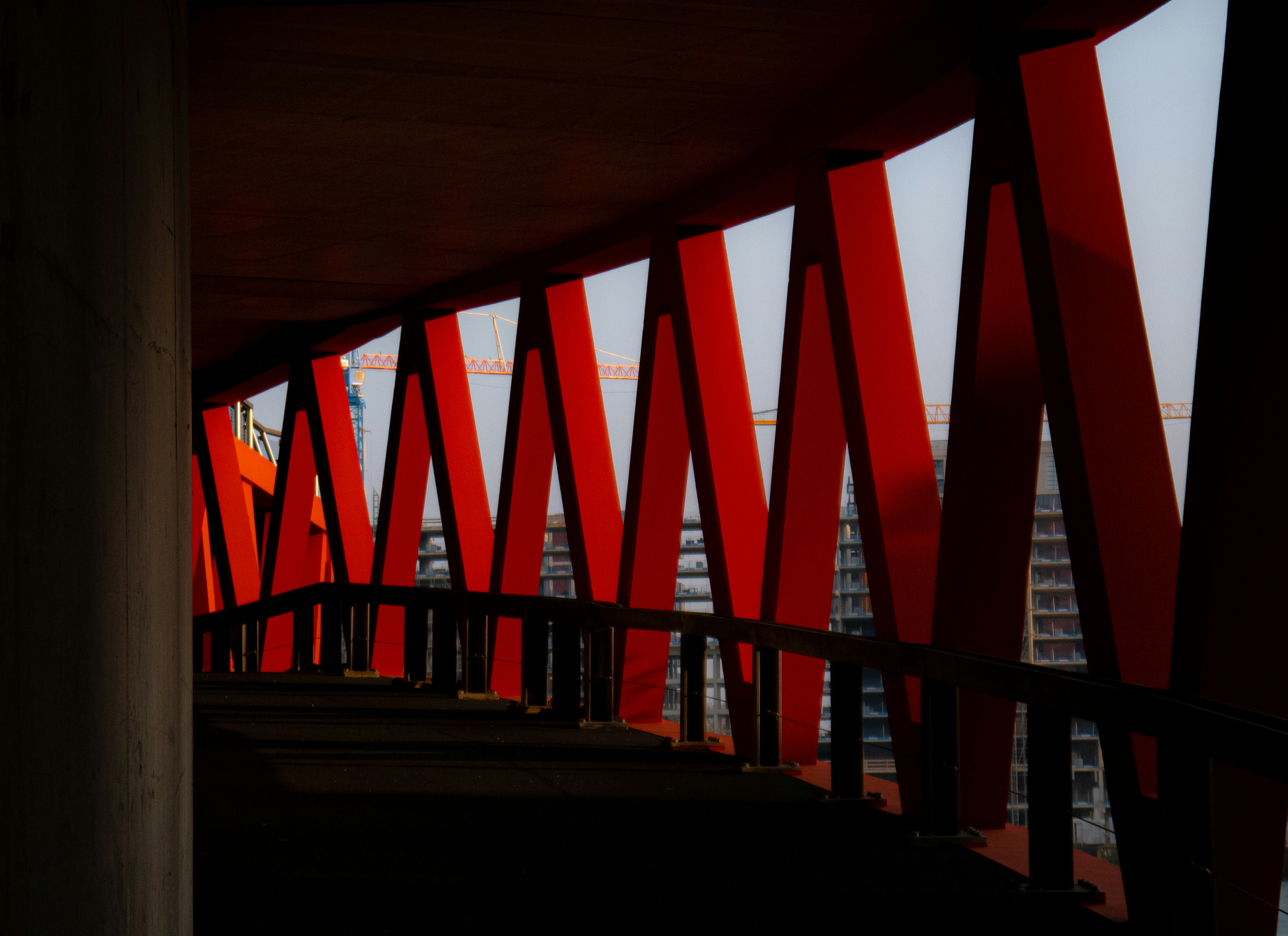 Red Trusses in the Shadowed Walk: An Architectural Corridor