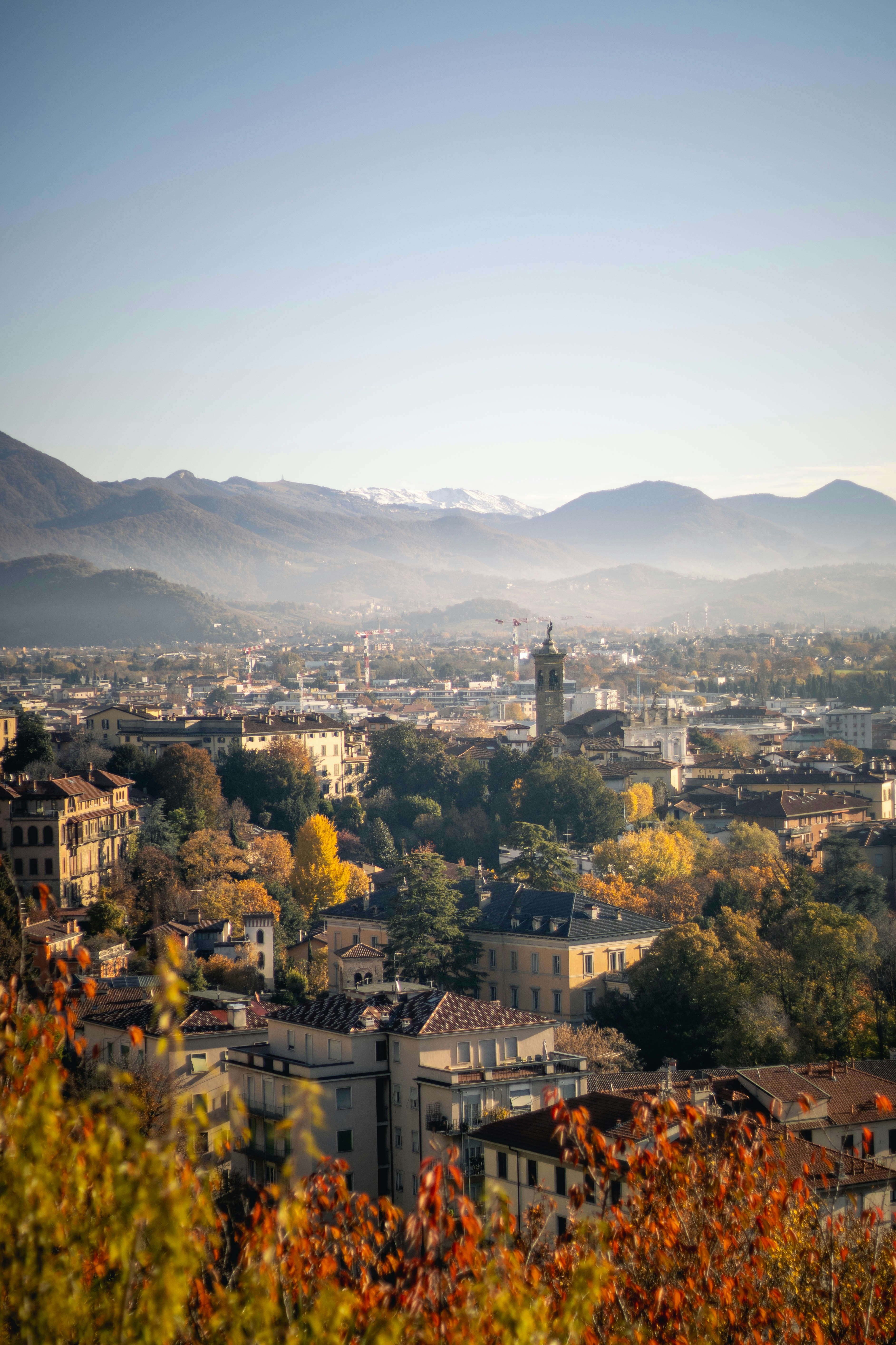 Panoramic view of a town nestled in a valley with autumn foliage and distant mountains under a clear blue sky.