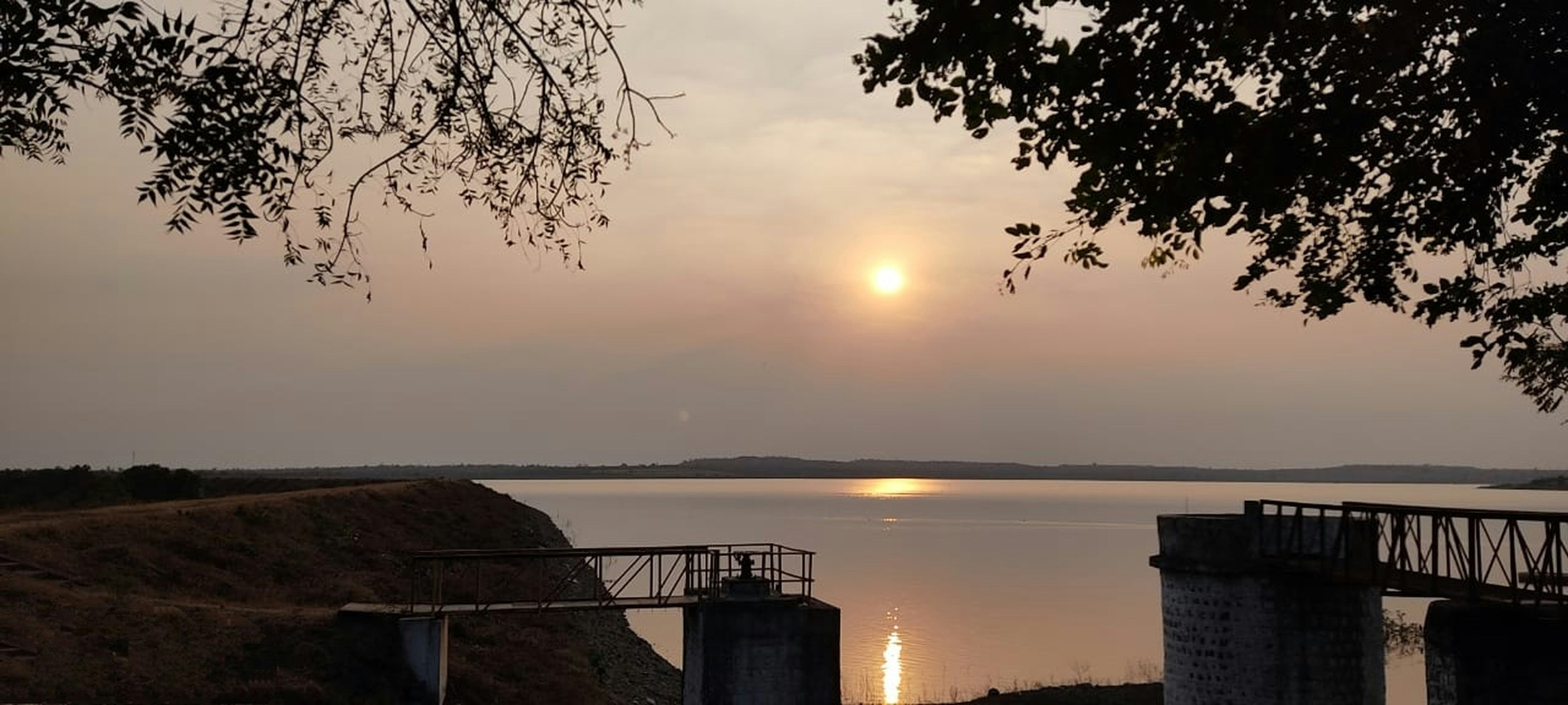 A sunset over a body of water with a bridge in the foreground photo ...