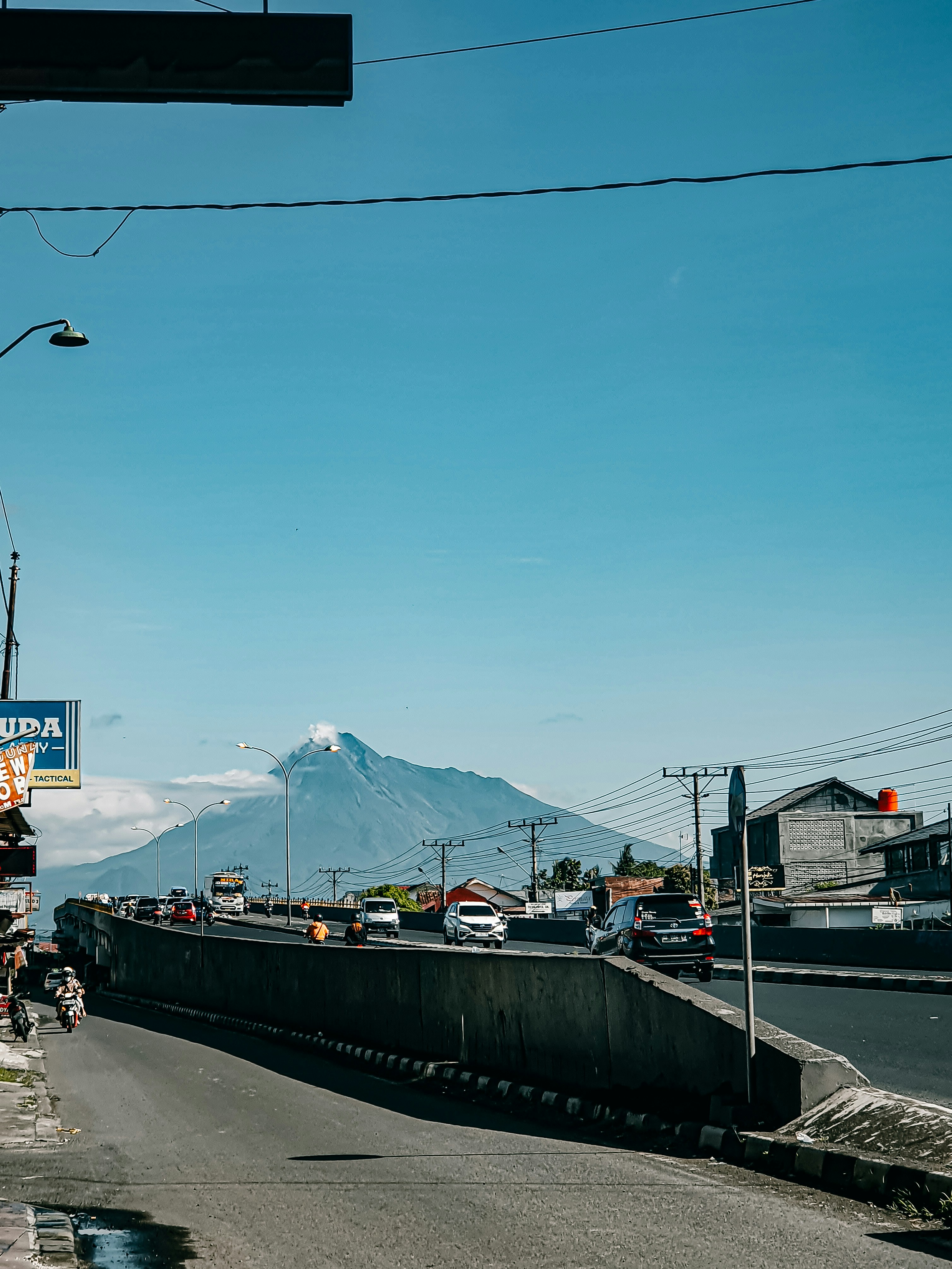 A bustling highway scene with vehicles navigating the road, framed by the imposing silhouette of a volcano under a clear blue sky.