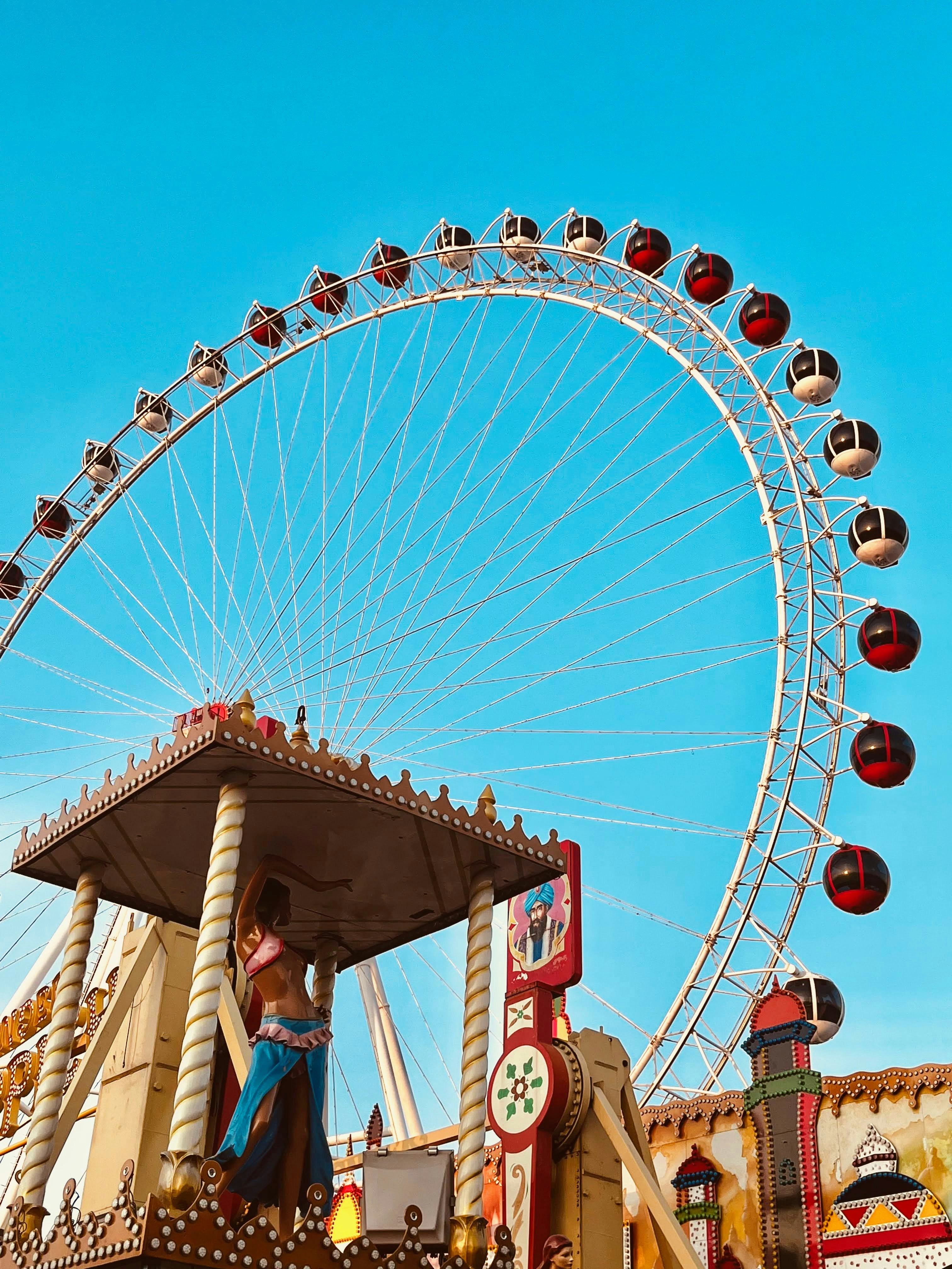 Towering Ferris wheel against a clear blue sky, with a vintage carousel visible in the foreground.