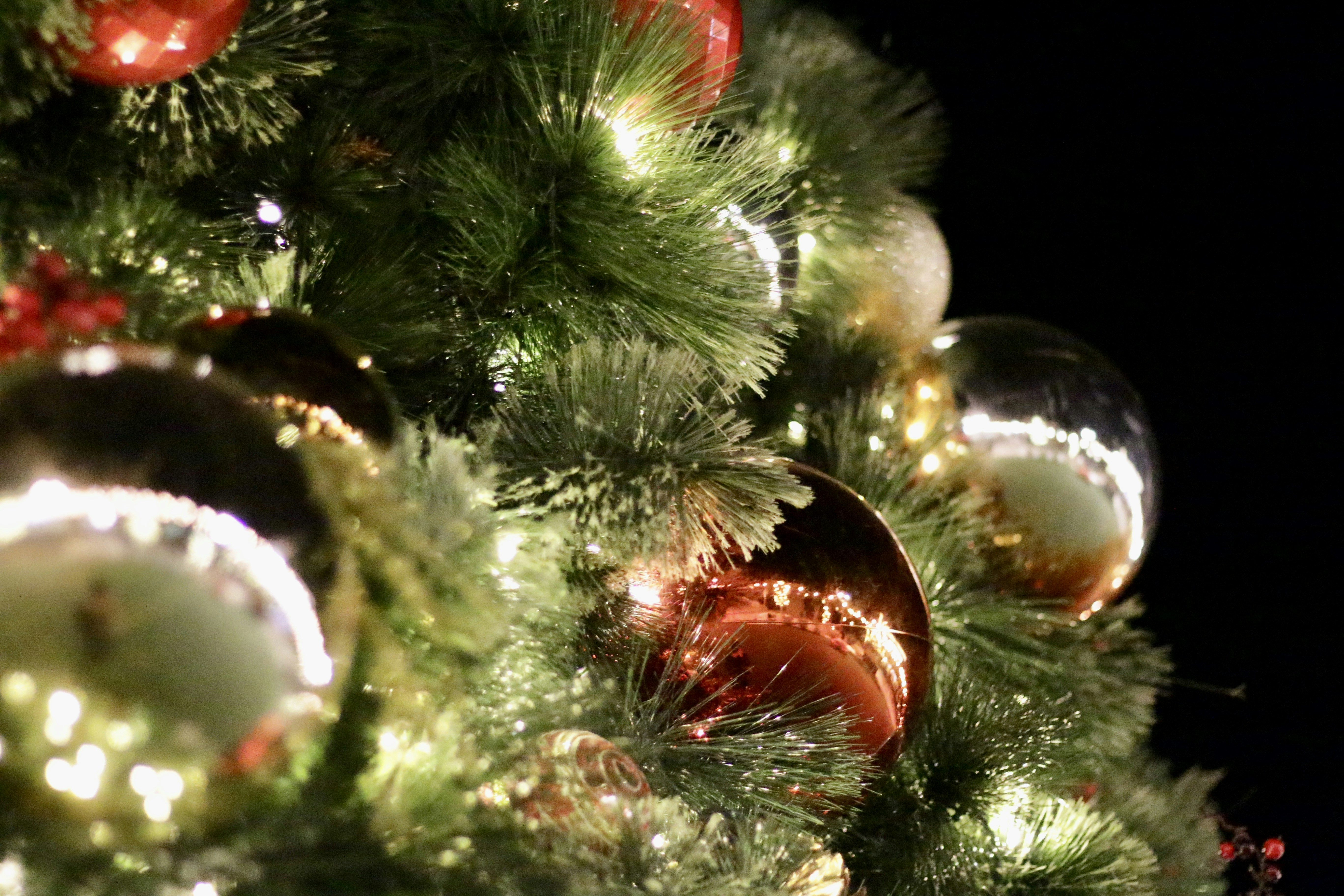 Christmas tree adorned with shiny ornaments and twinkling lights against a dark background.