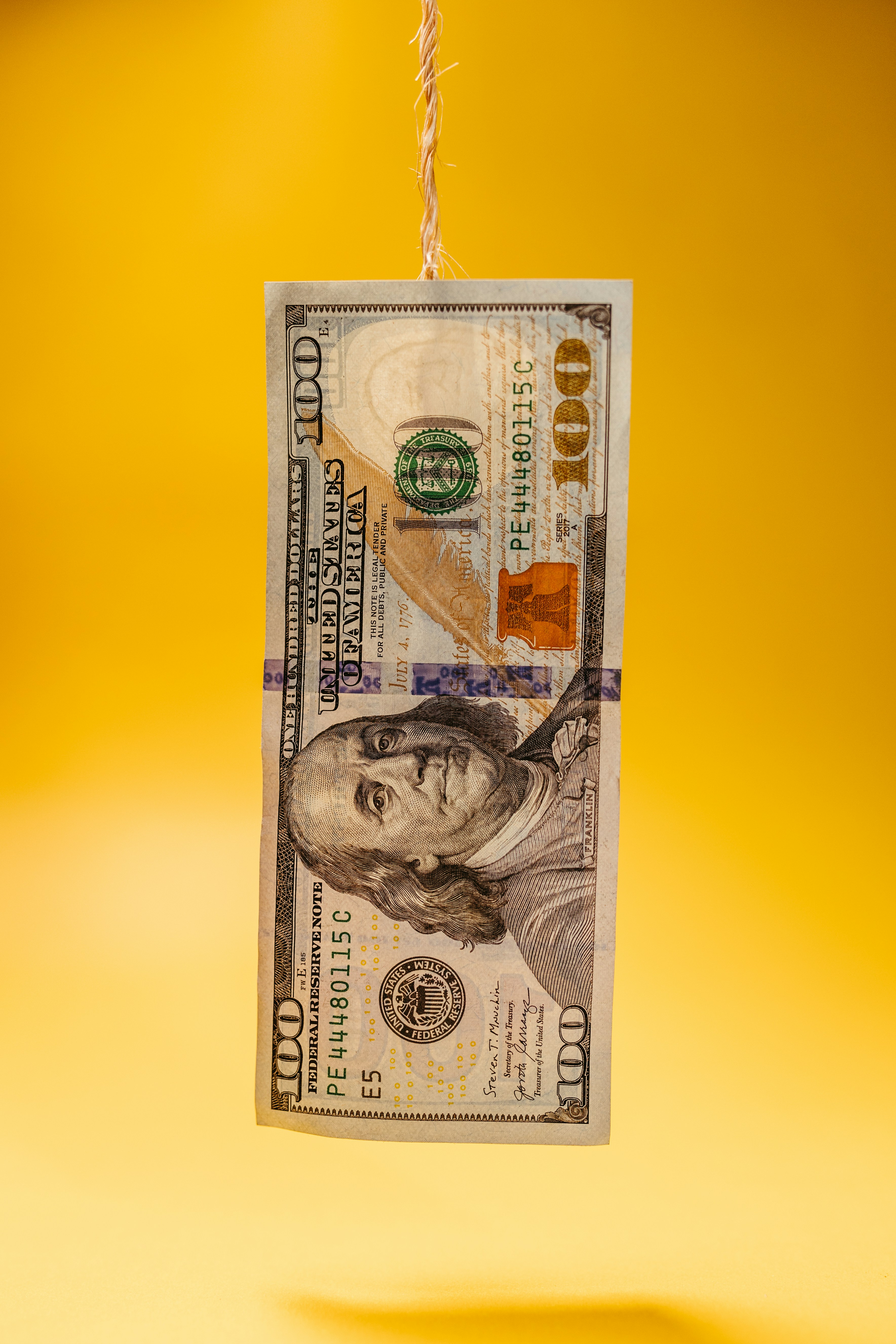 A dollar bill hanging from a string on a yellow background photo – Free ...
