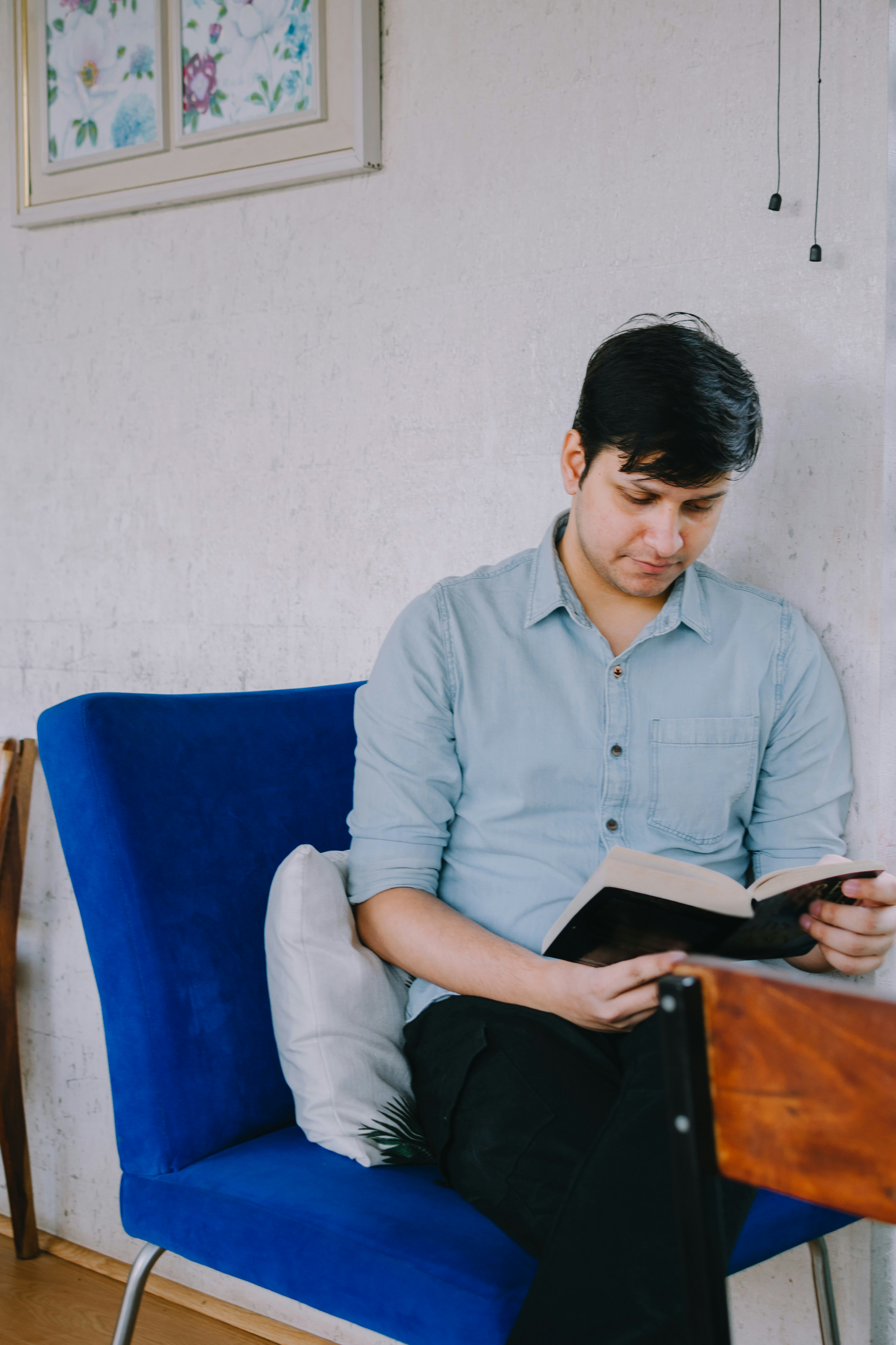 A man sitting on a blue chair reading a book photo – Free Image on Unsplash