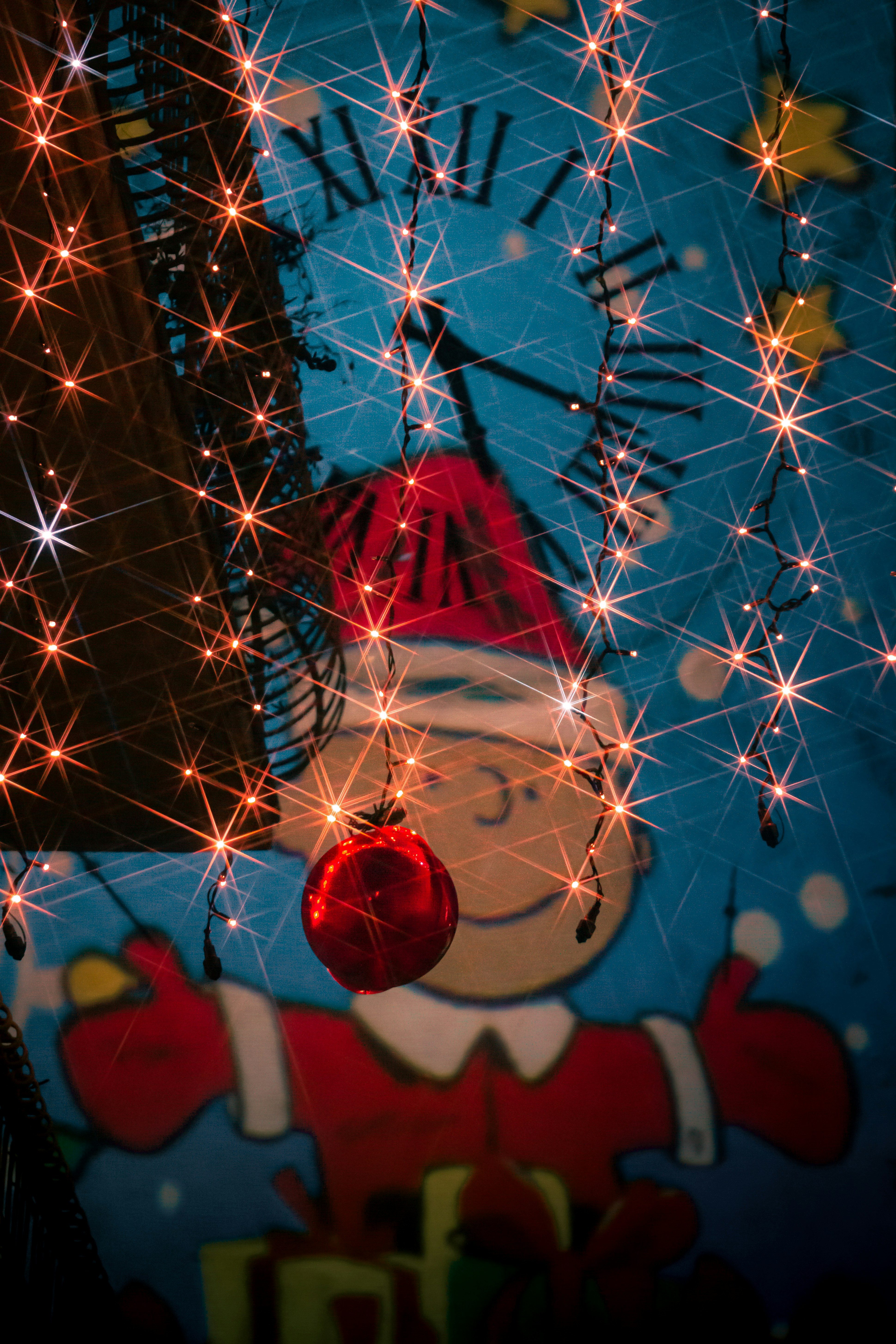 A vibrant red ornament hangs amidst sparkling lights, with a cheerful snowman illustration in the background, evoking a festive atmosphere.