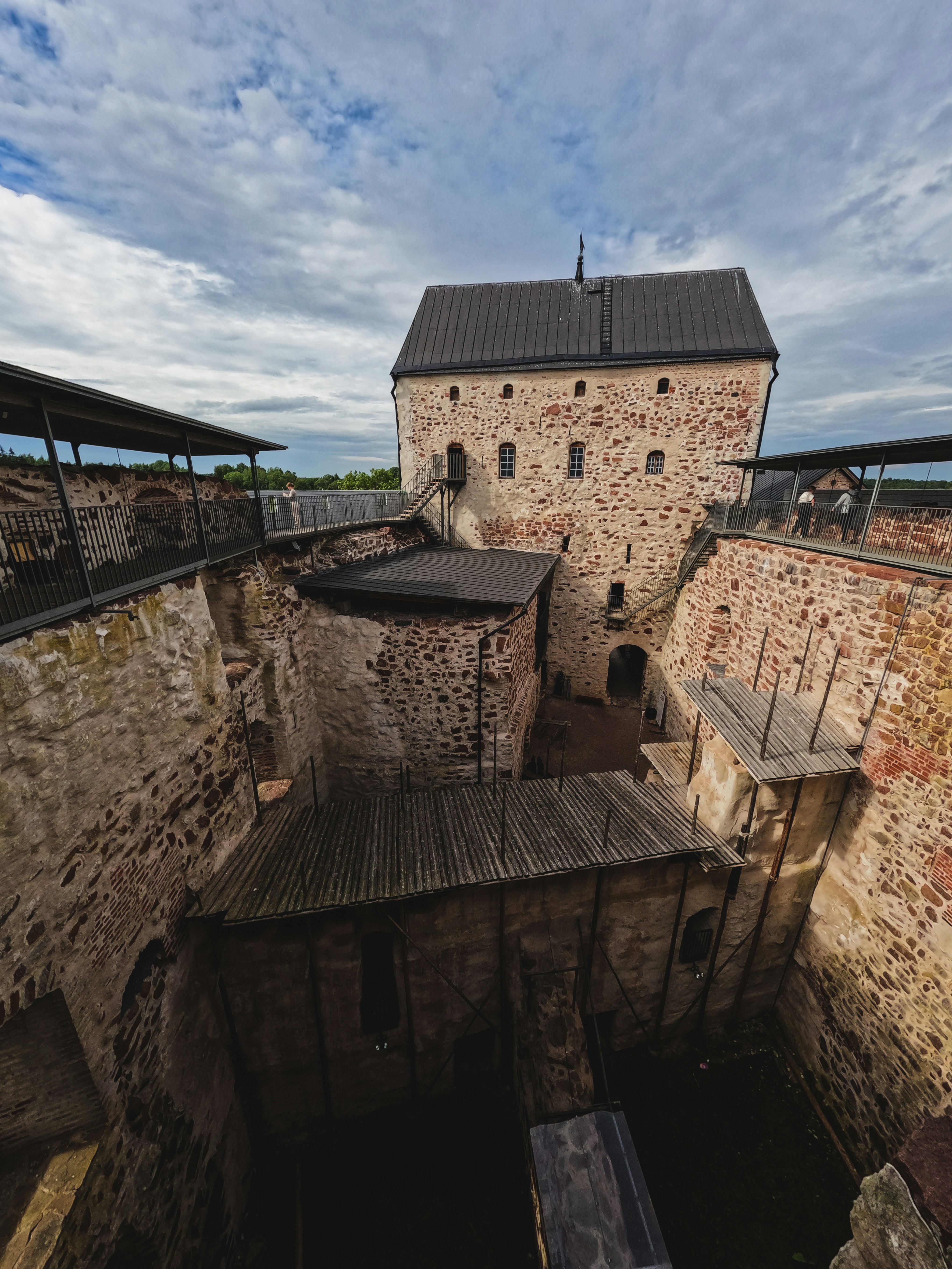 Ancient stone castle ruins with wooden walkways and a cloudy sky above, showcasing the remnants of a bygone era.