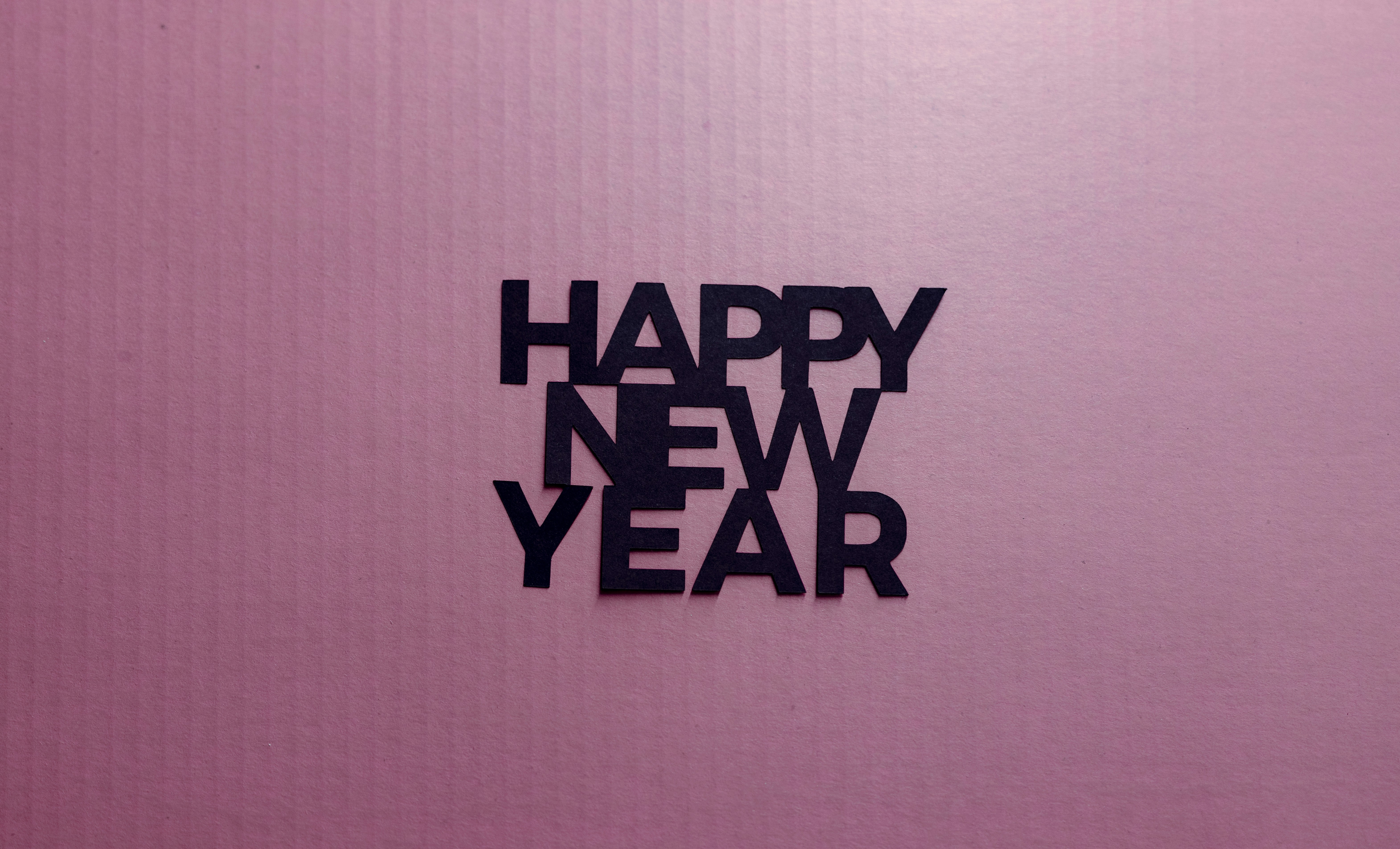 Black letters spelling 'HAPPY NEW YEAR' on a soft pink background, creating a vibrant and cheerful atmosphere.