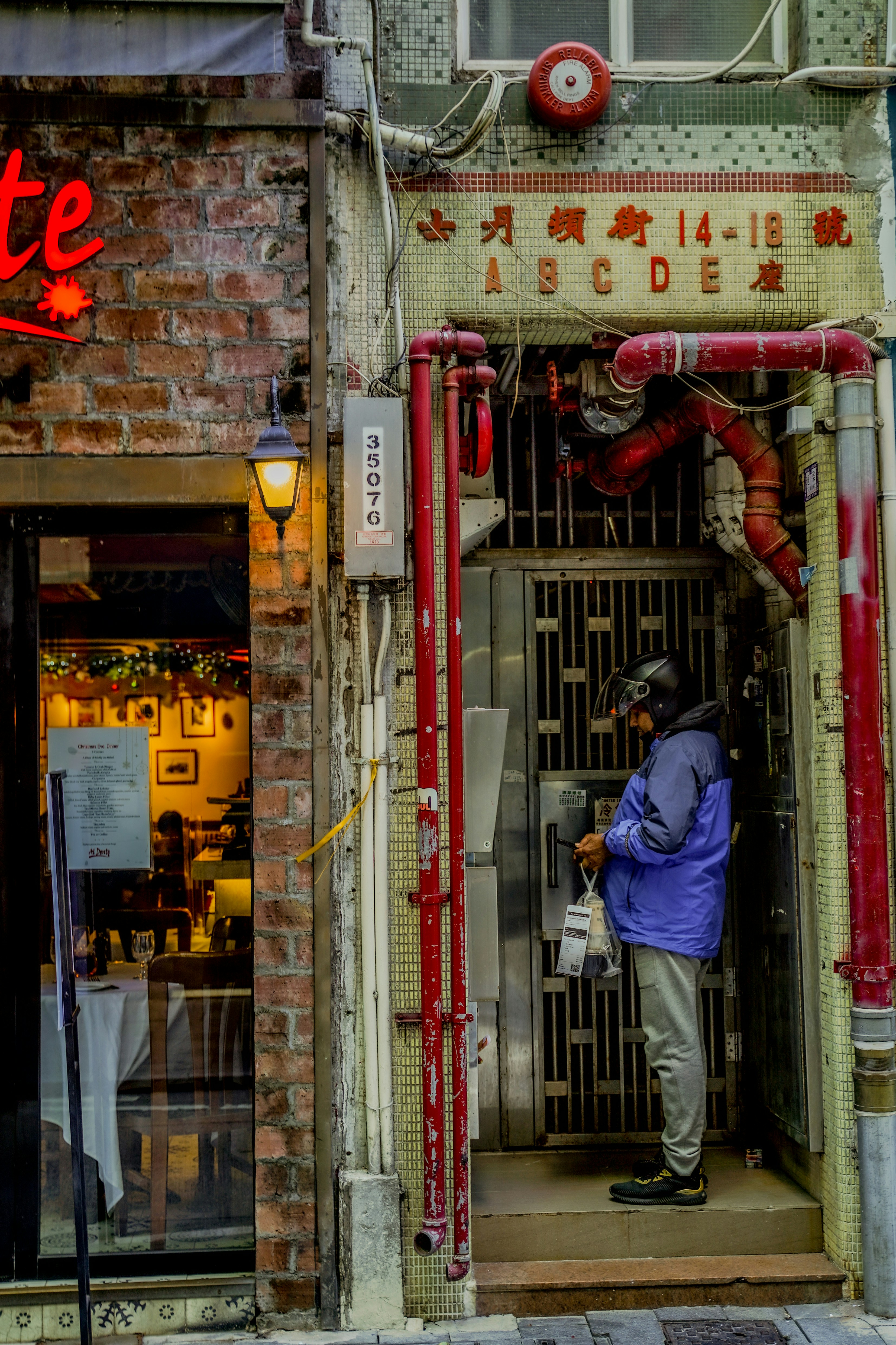Blue-Jacketed Figure at a Red-Piped Threshold in a Chinatown Alley