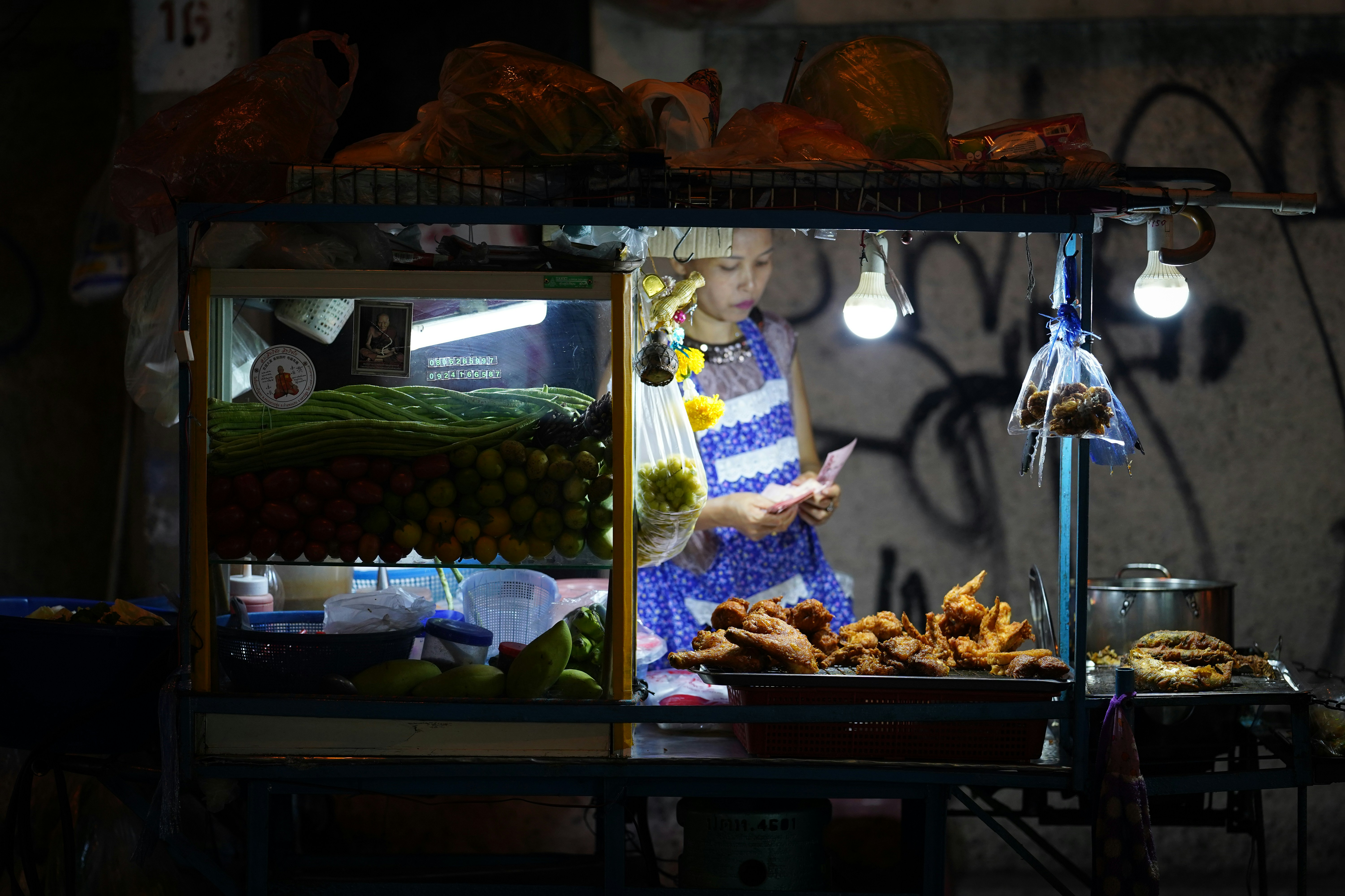 Blue-Draped Vendor at a Quiet Night Market Stall Under a Single Bulb