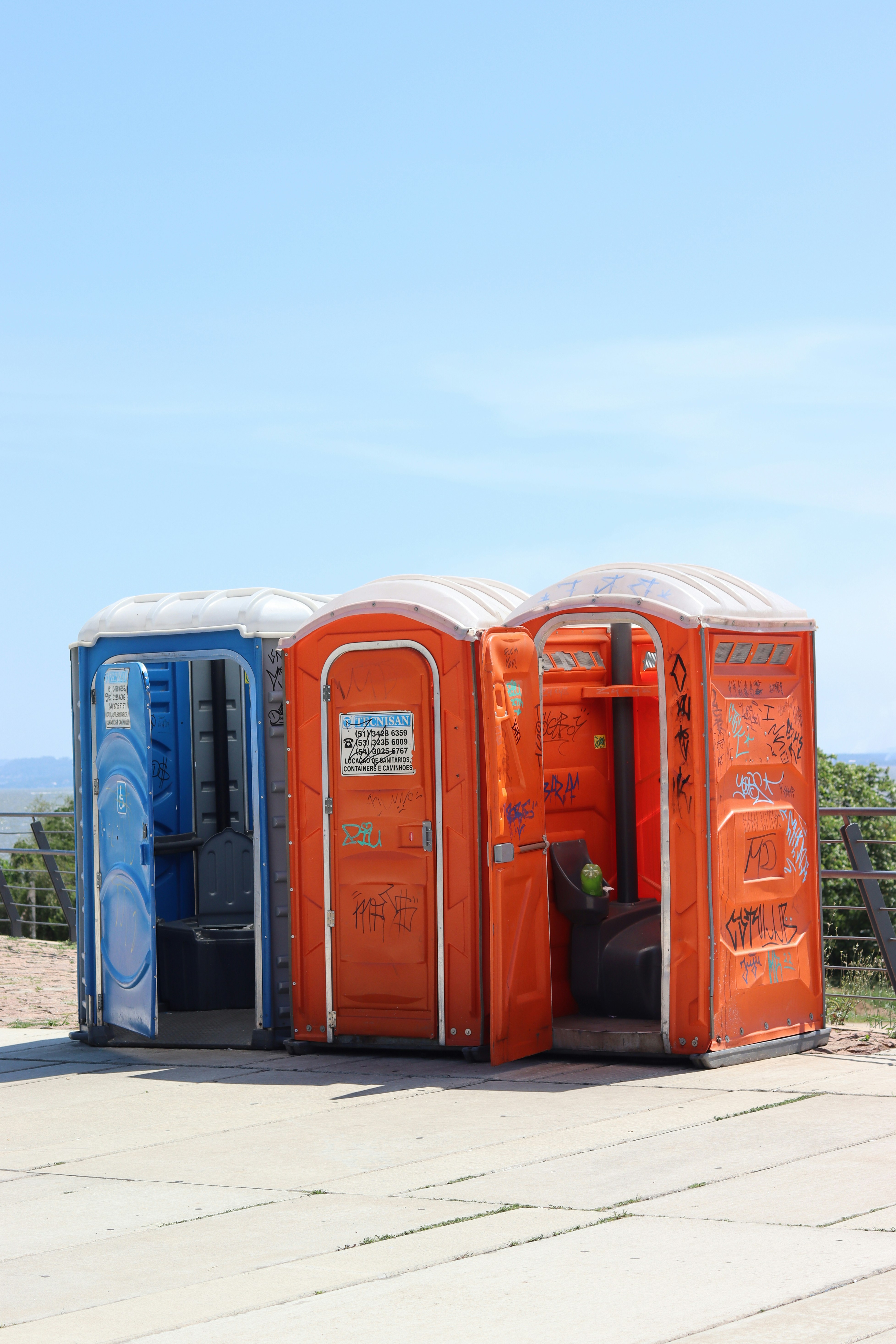 A group of three portable toilets sitting on top of a sidewalk photo ...