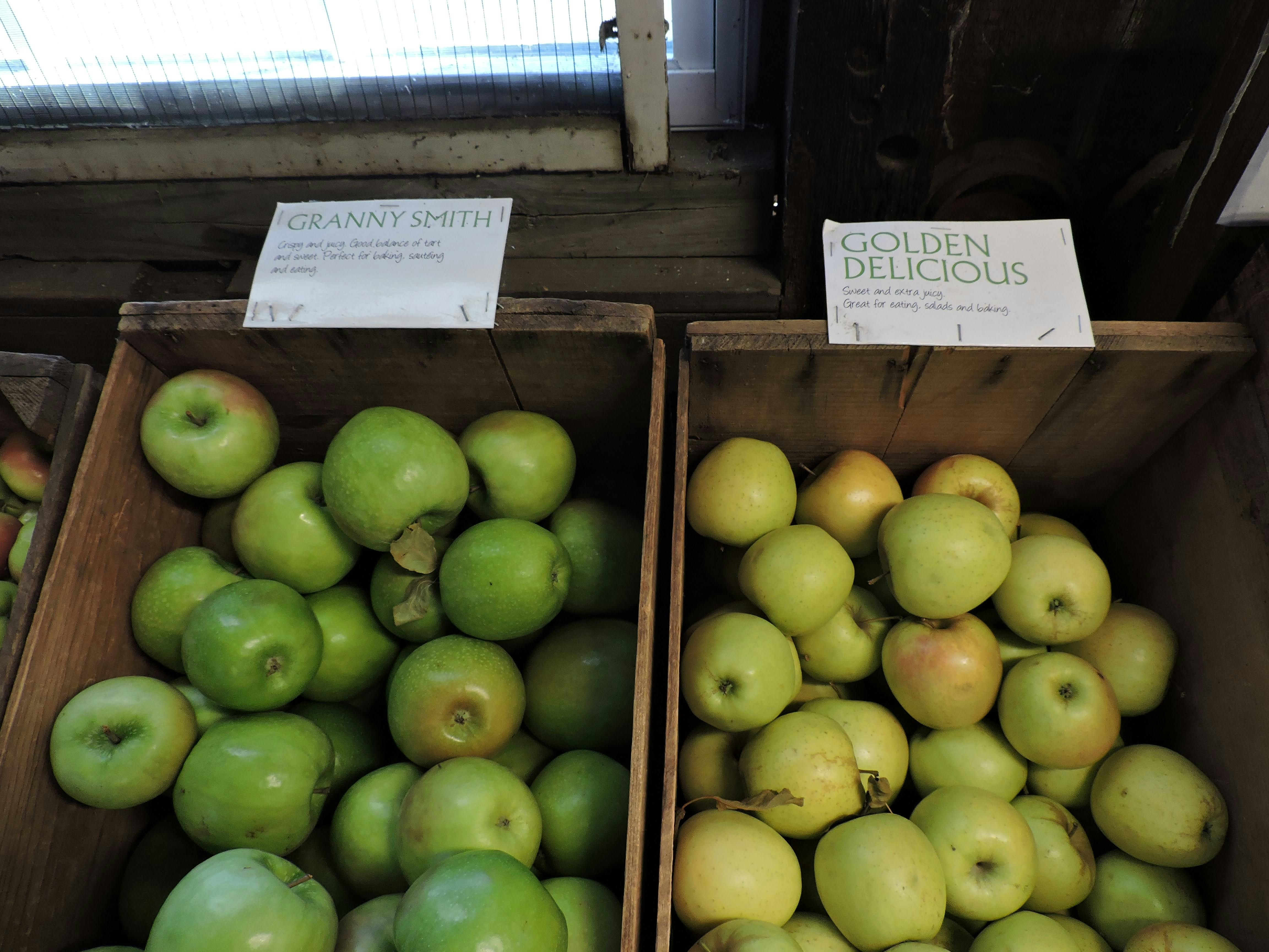 Two wooden crates overflow with apples—left Granny Smith, right Golden Delicious—displayed in a market setting with soft daylight.