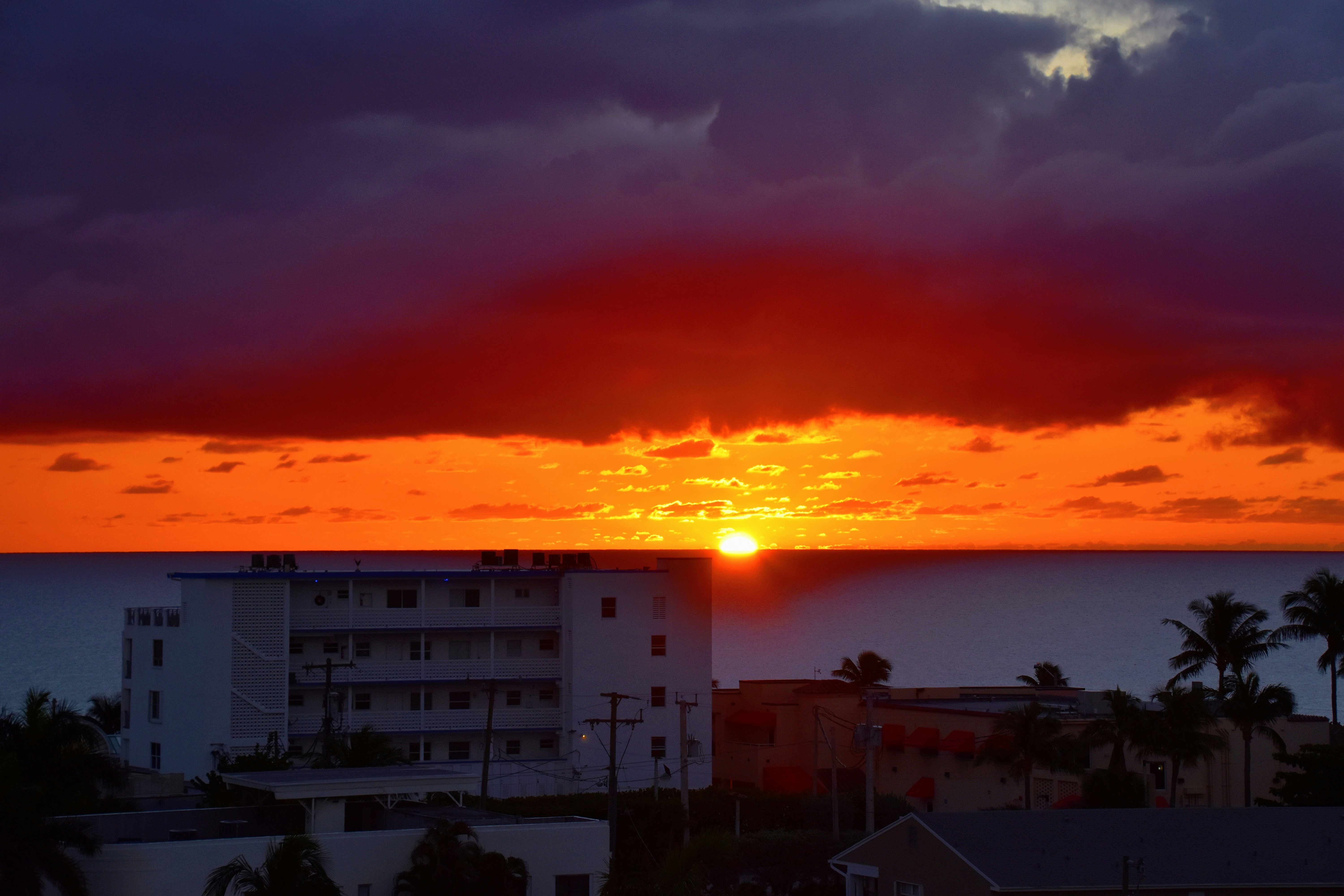 El sol se está poniendo sobre el océano y los edificios foto – Imagen ...