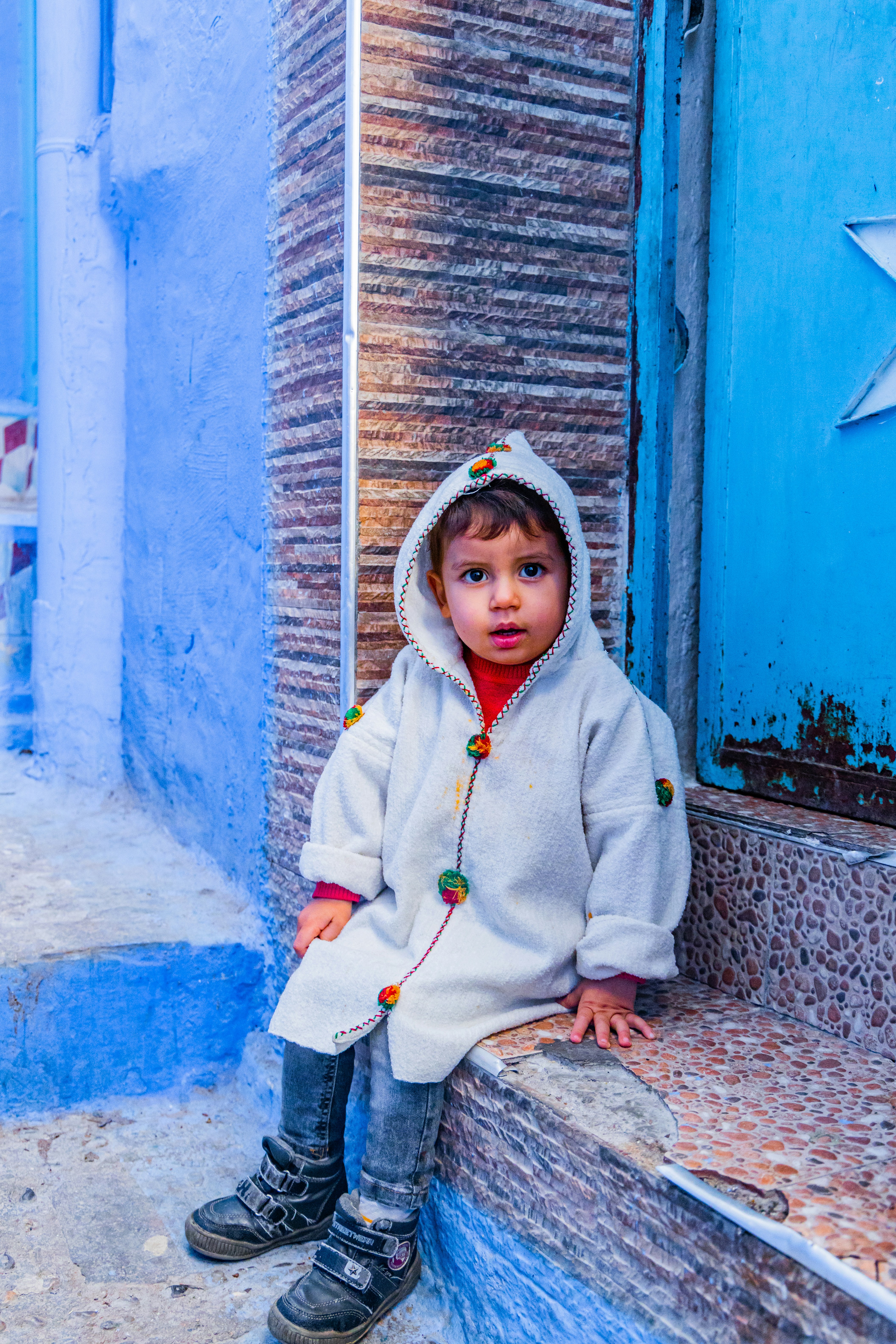 a little boy sitting on a ledge in front of a building