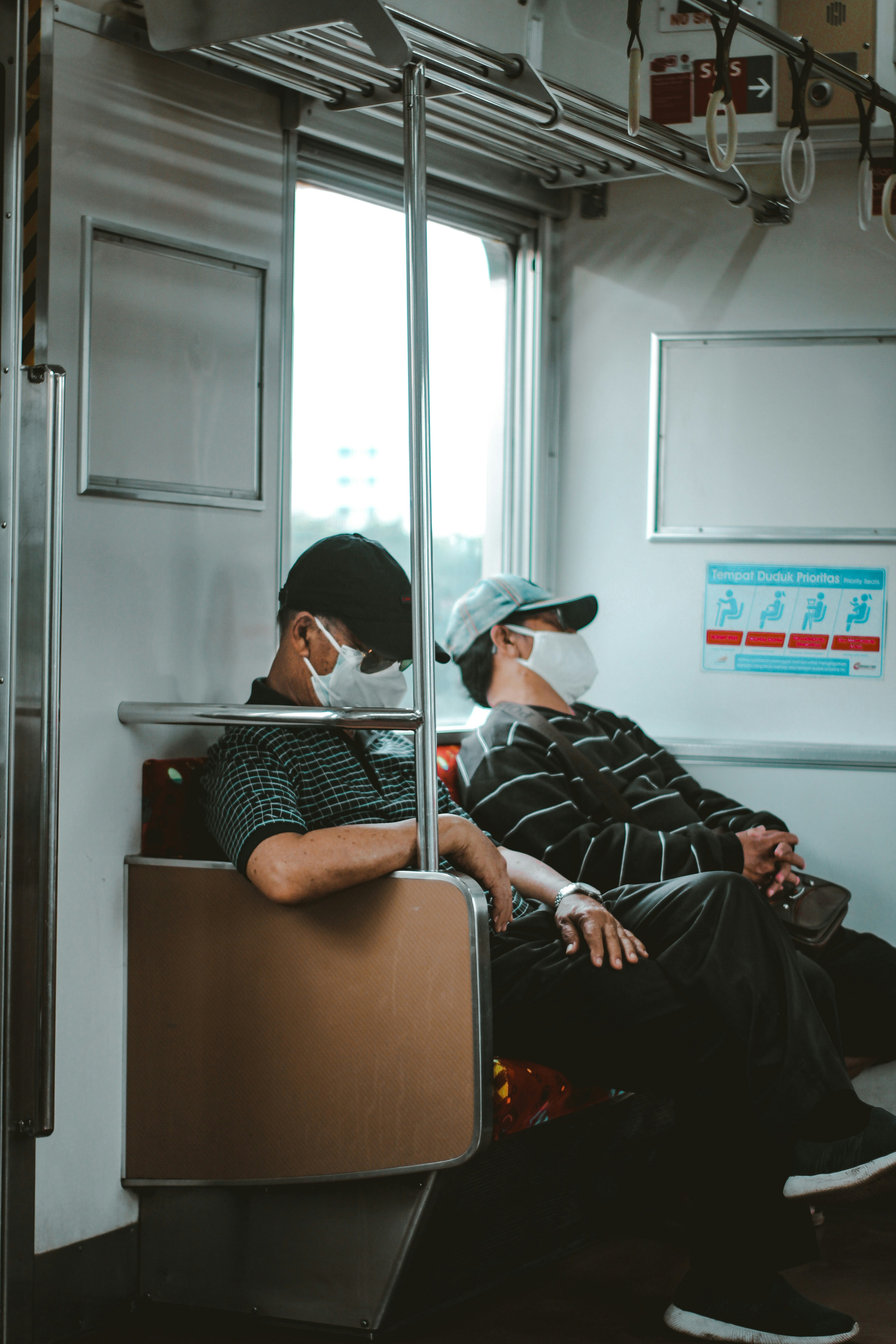 Doorside Solace: Masked Commuters Rest in a Sunlit Train Car