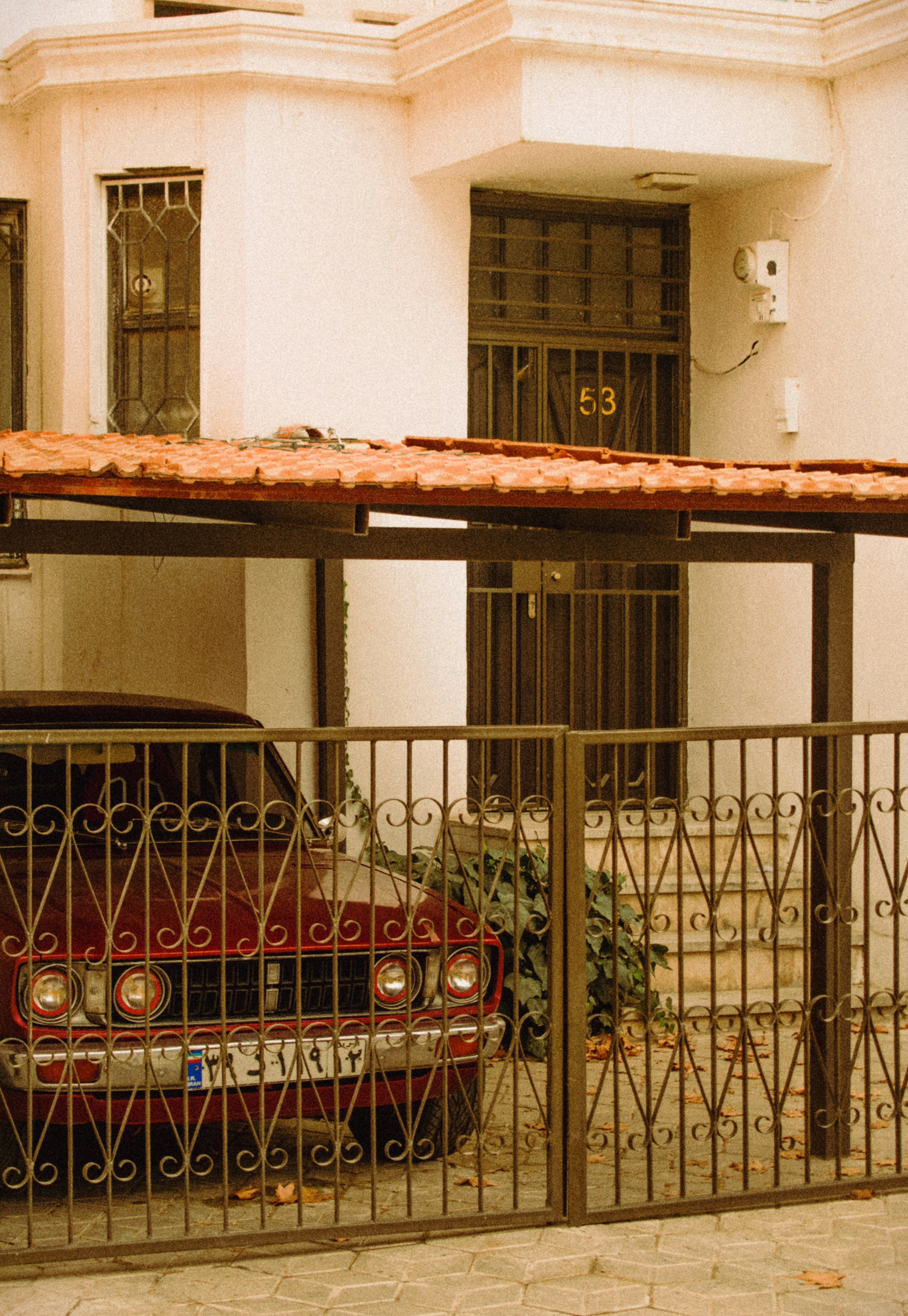 Red Classic Car Beneath a Clay-Tiled Carport Behind Ornate Ironwork