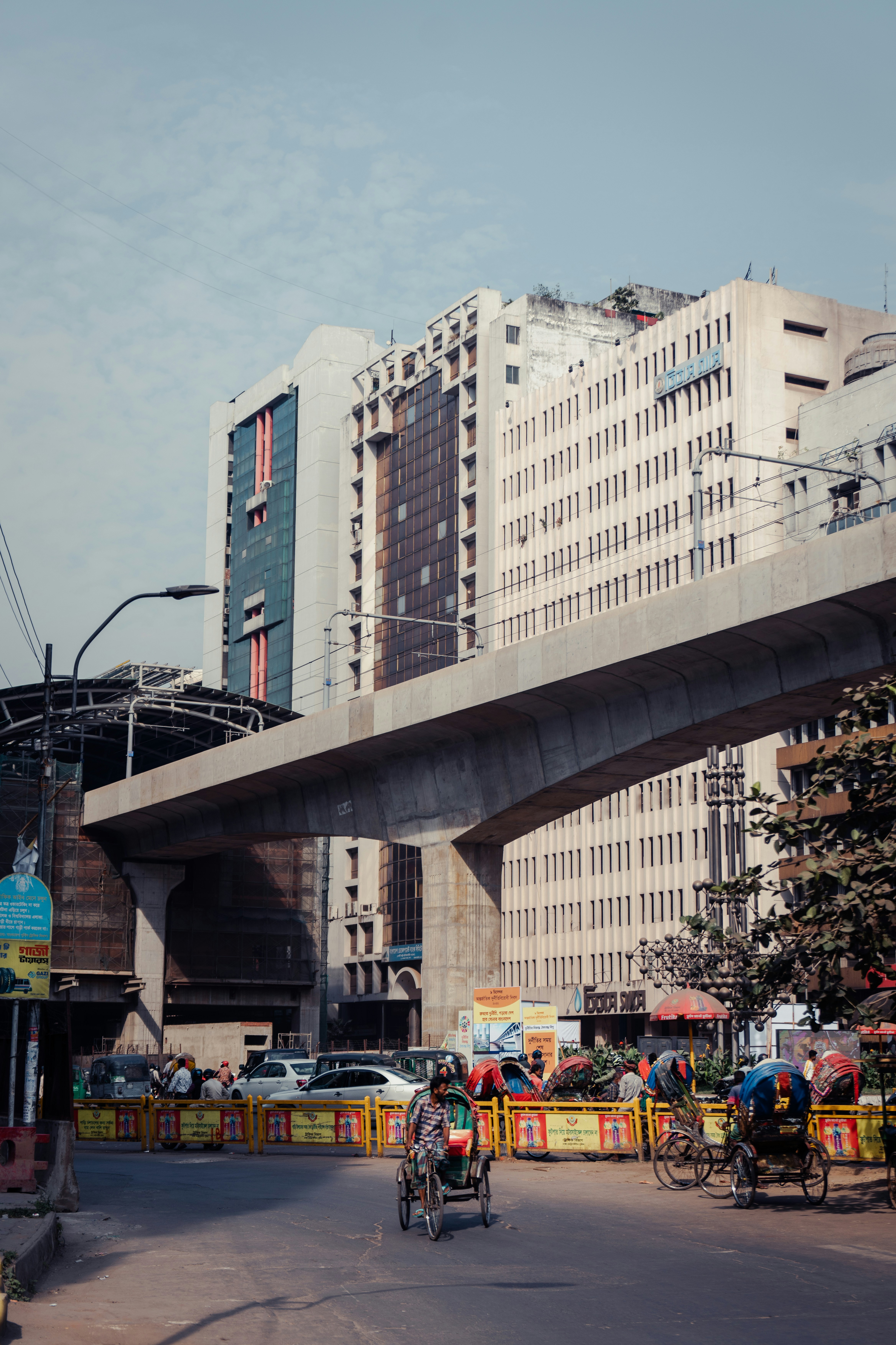 Busy intersection featuring a mix of modern skyscrapers and traditional rickshaws under a concrete overpass.