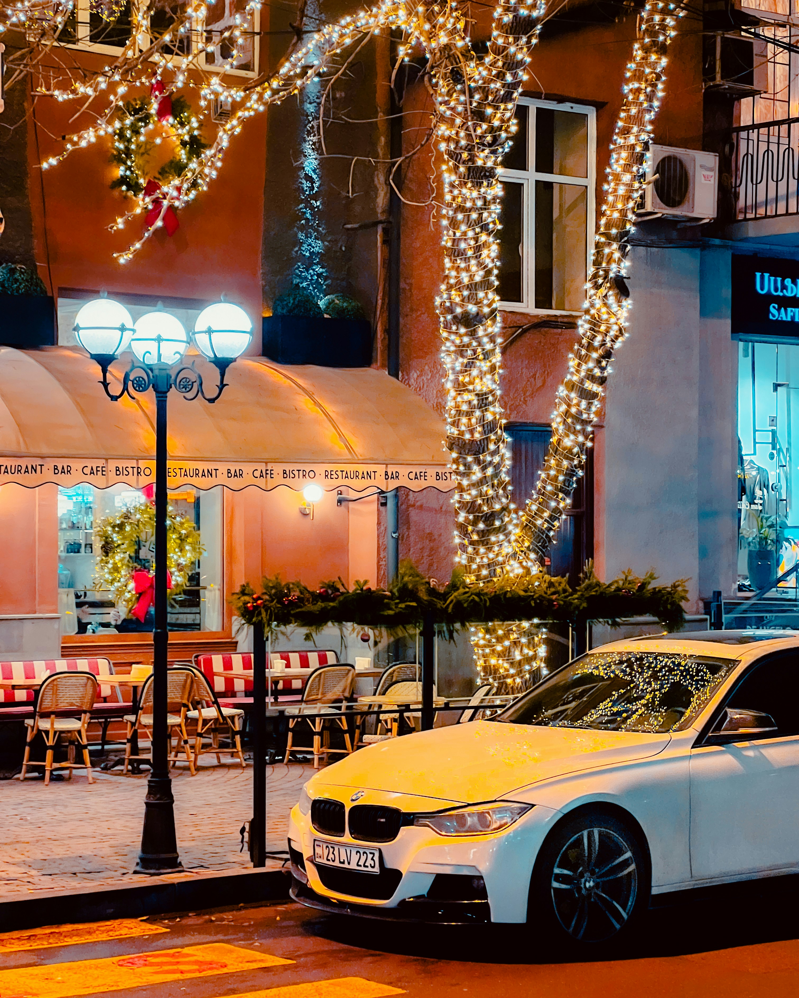 Ivory BMW Under Holiday Glow by a Neon- warmly lit Cafe Row