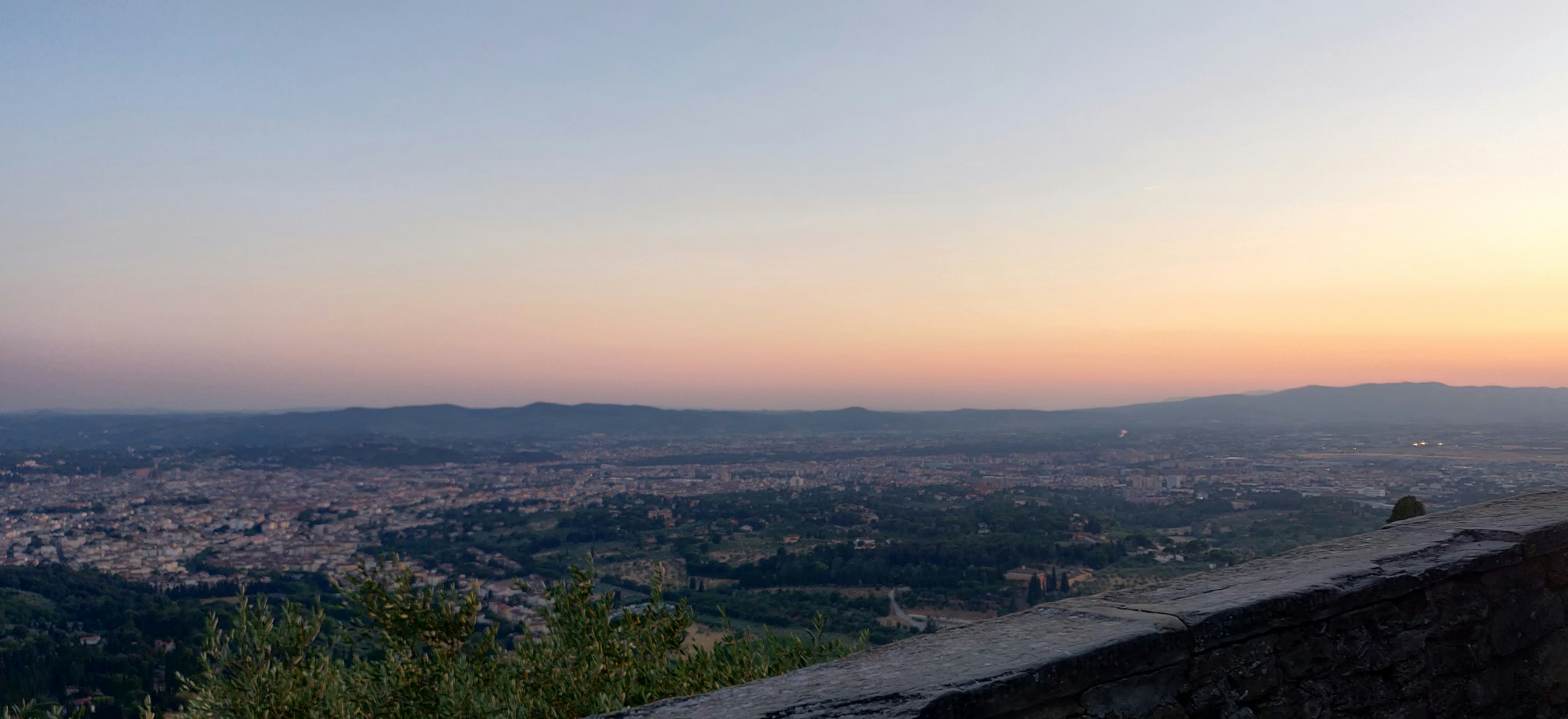 Expansive view of Florence at dusk with a soft gradient sky and lush greenery in the foreground.