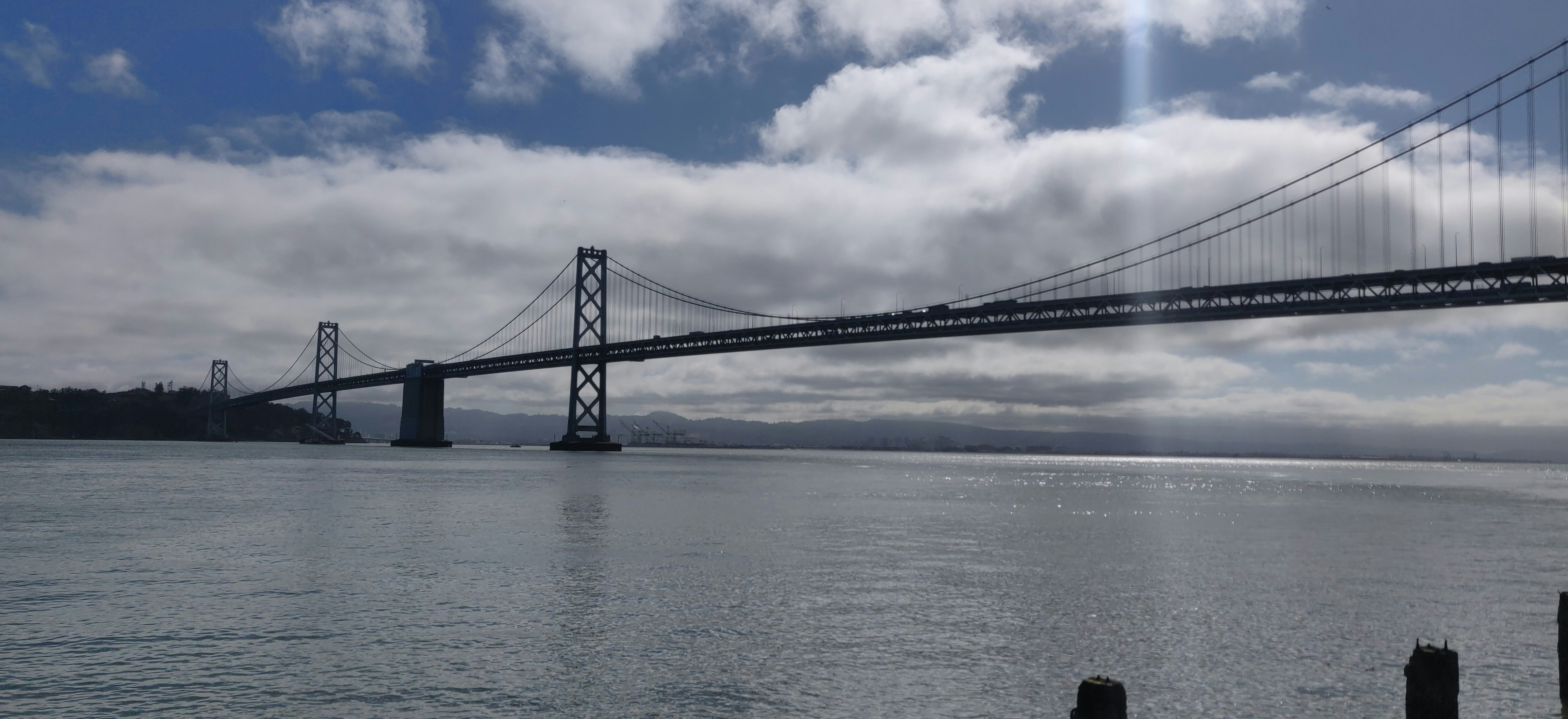 Bay Bridge stretching across calm waters under a cloudy sky, showcasing the interplay of light and reflections.